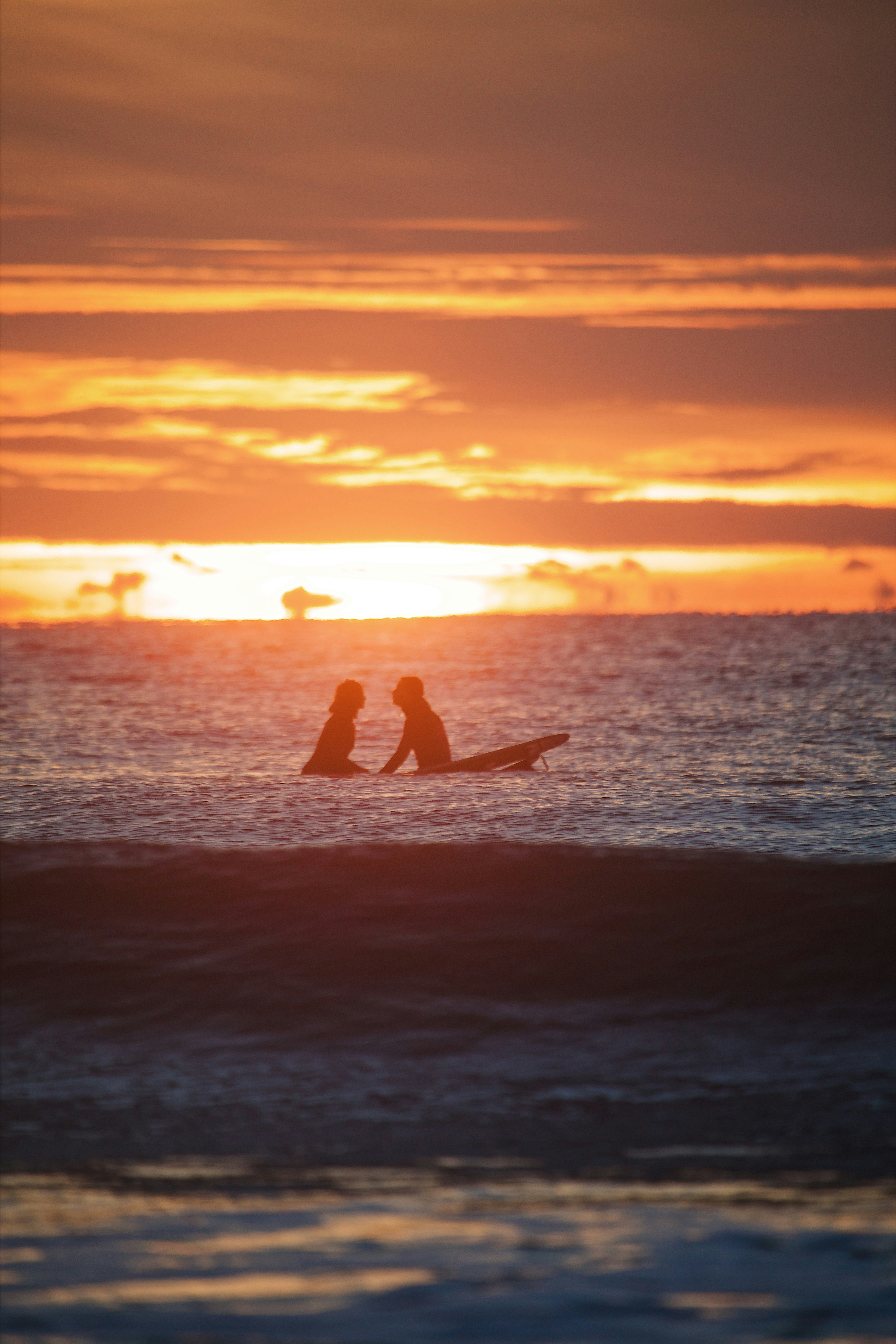 Two silhouettes in a surfer’s boat share a sunset moment over a calm horizon
