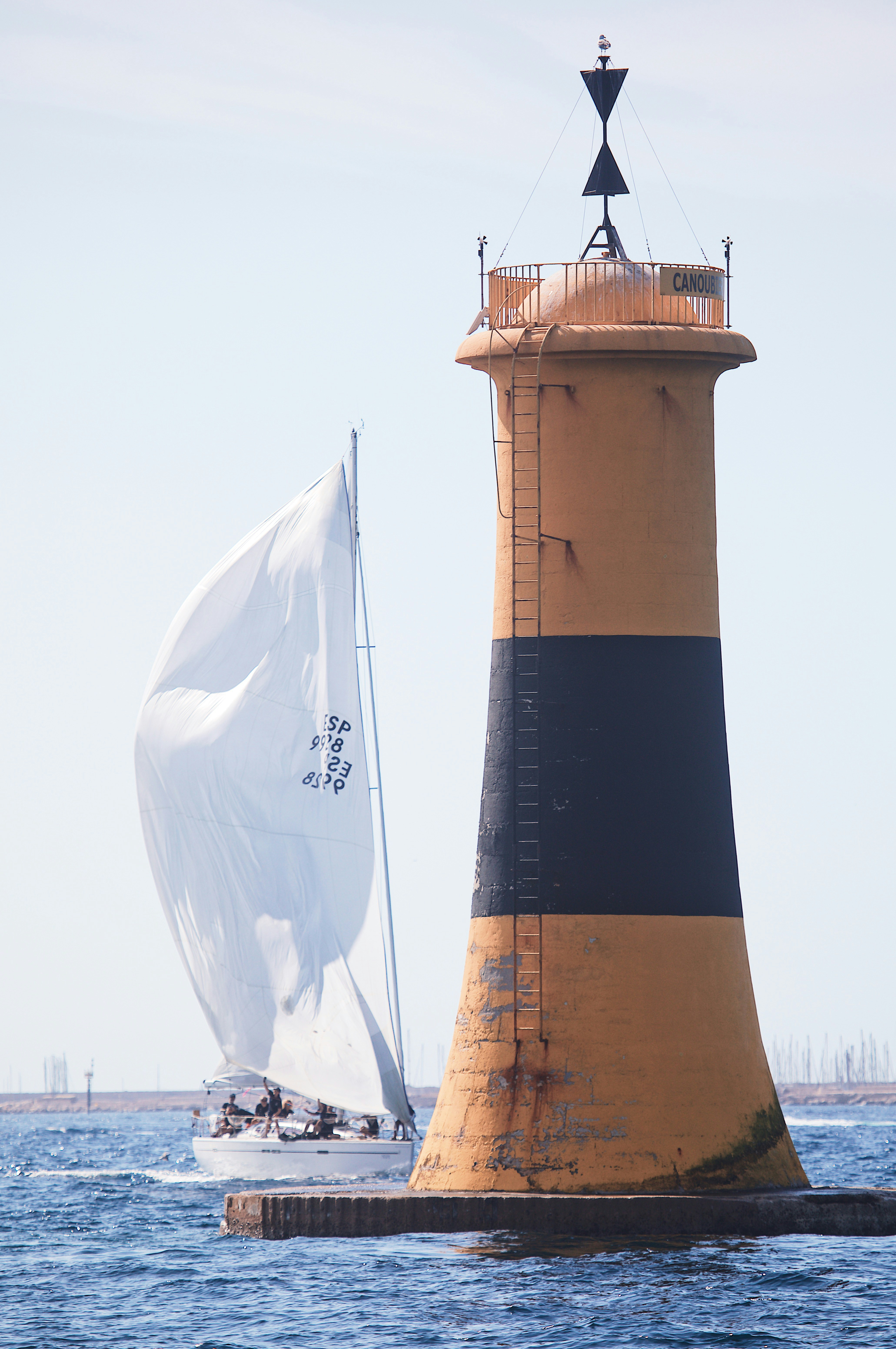 Sail and beacon: a lighthouse in the sea with a sailboat gliding past