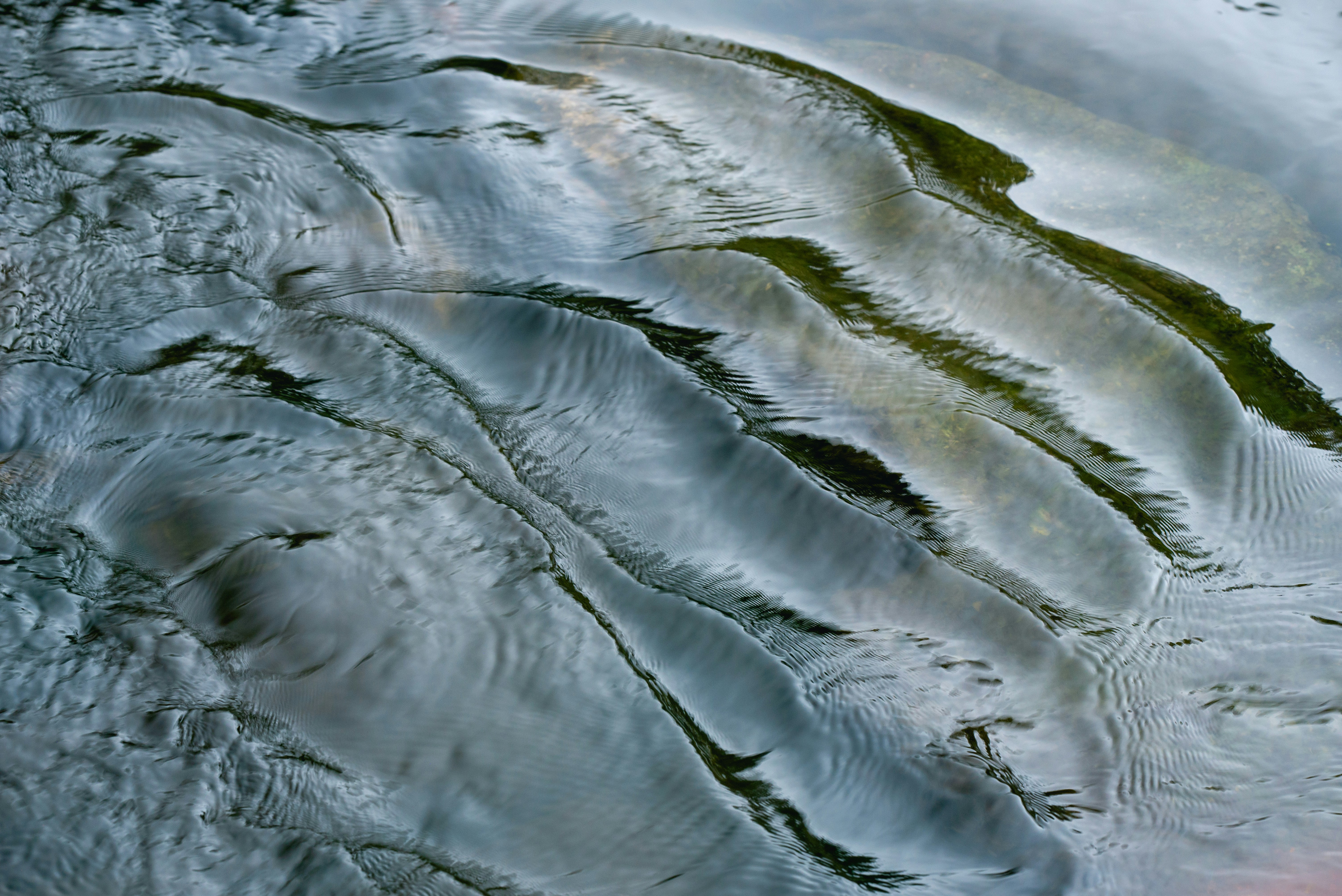 Textured terraces and ripple patterns carved by water across a shallow pool, highlighting layered contours and mineral hues. A minimal, abstract landscape focusing on surface detail.