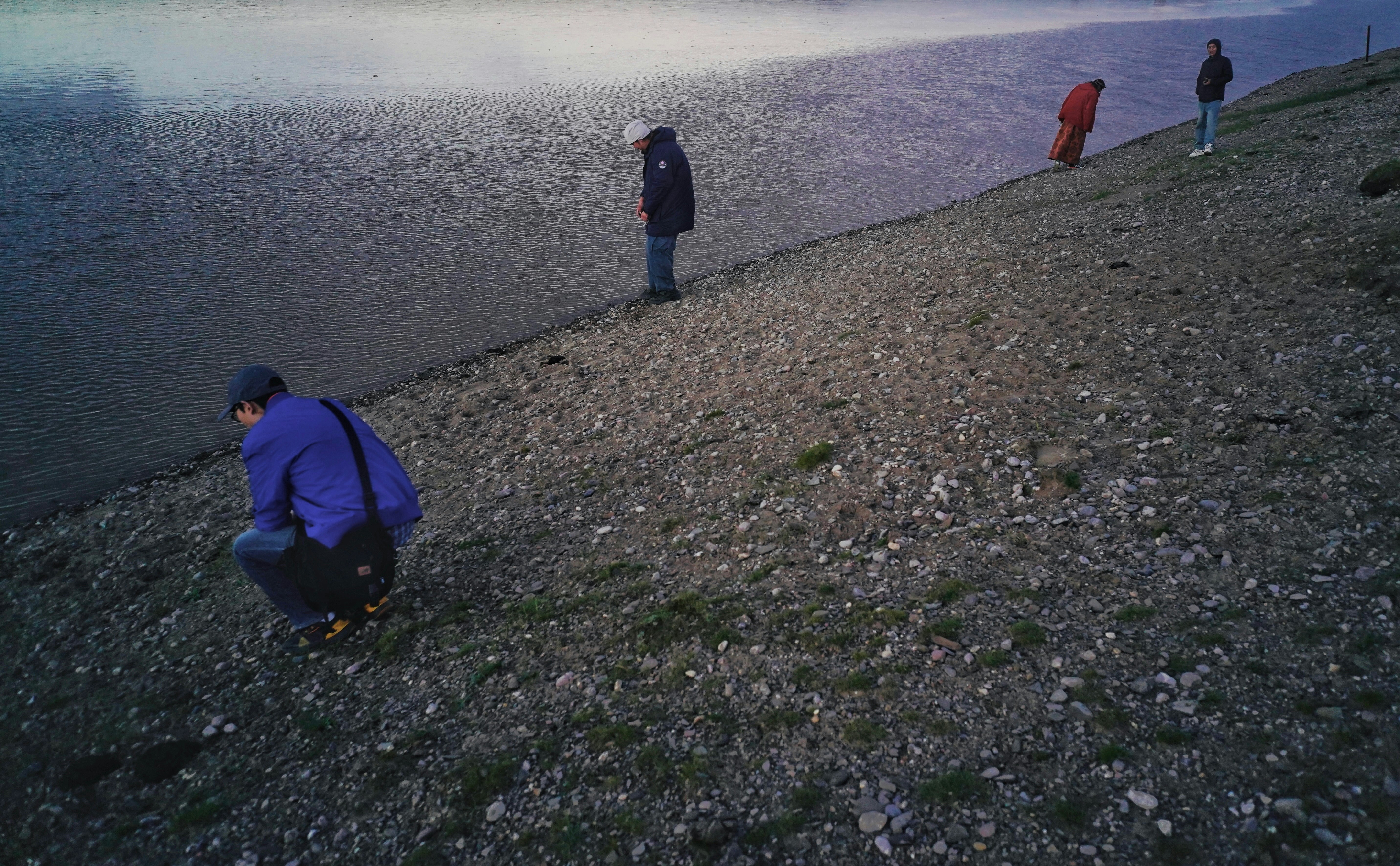 Cold shoreline silhouettes: anglers along a pebbled slope