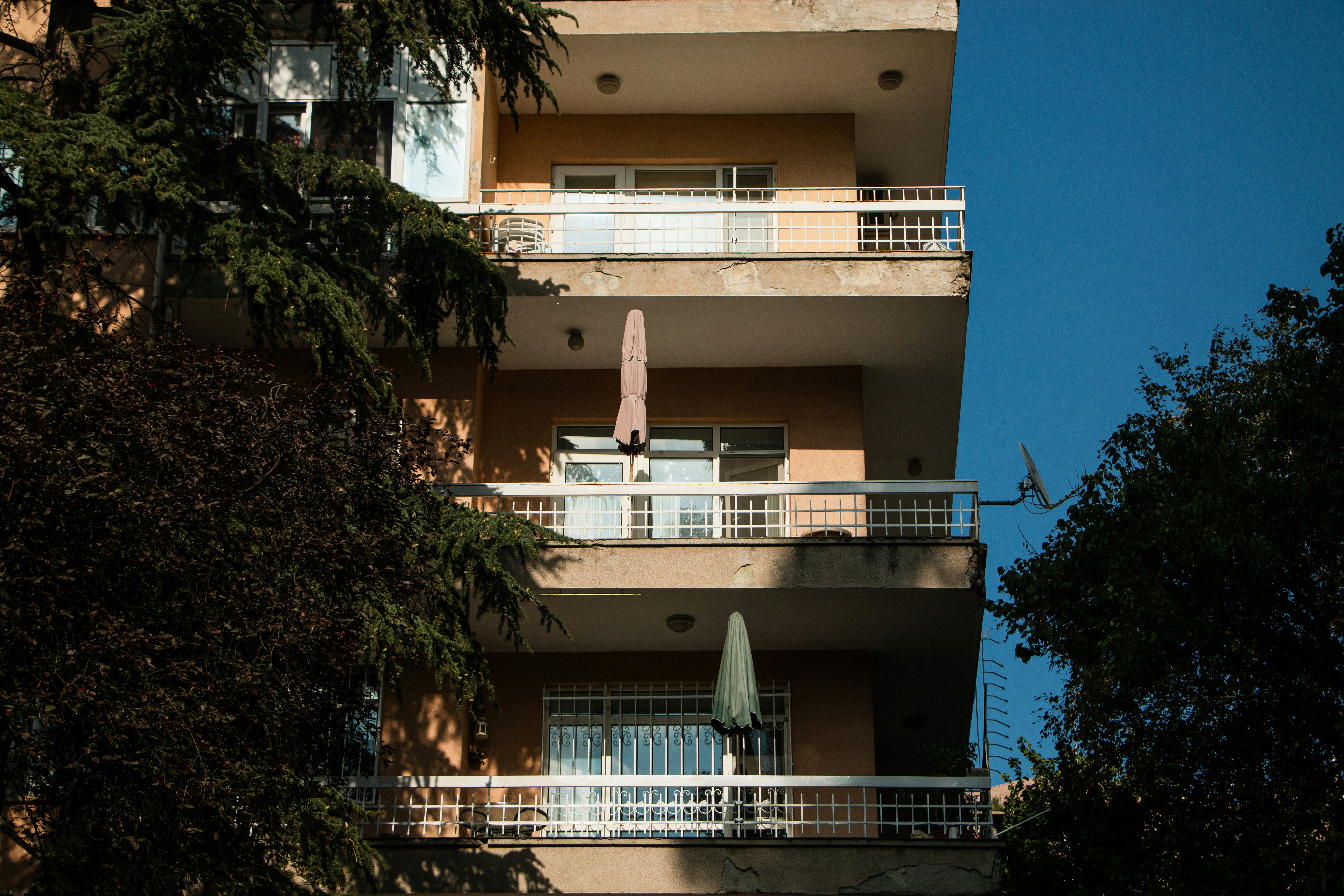 Balconies in sunlight: a peach apartment block amid deep shadow and trees