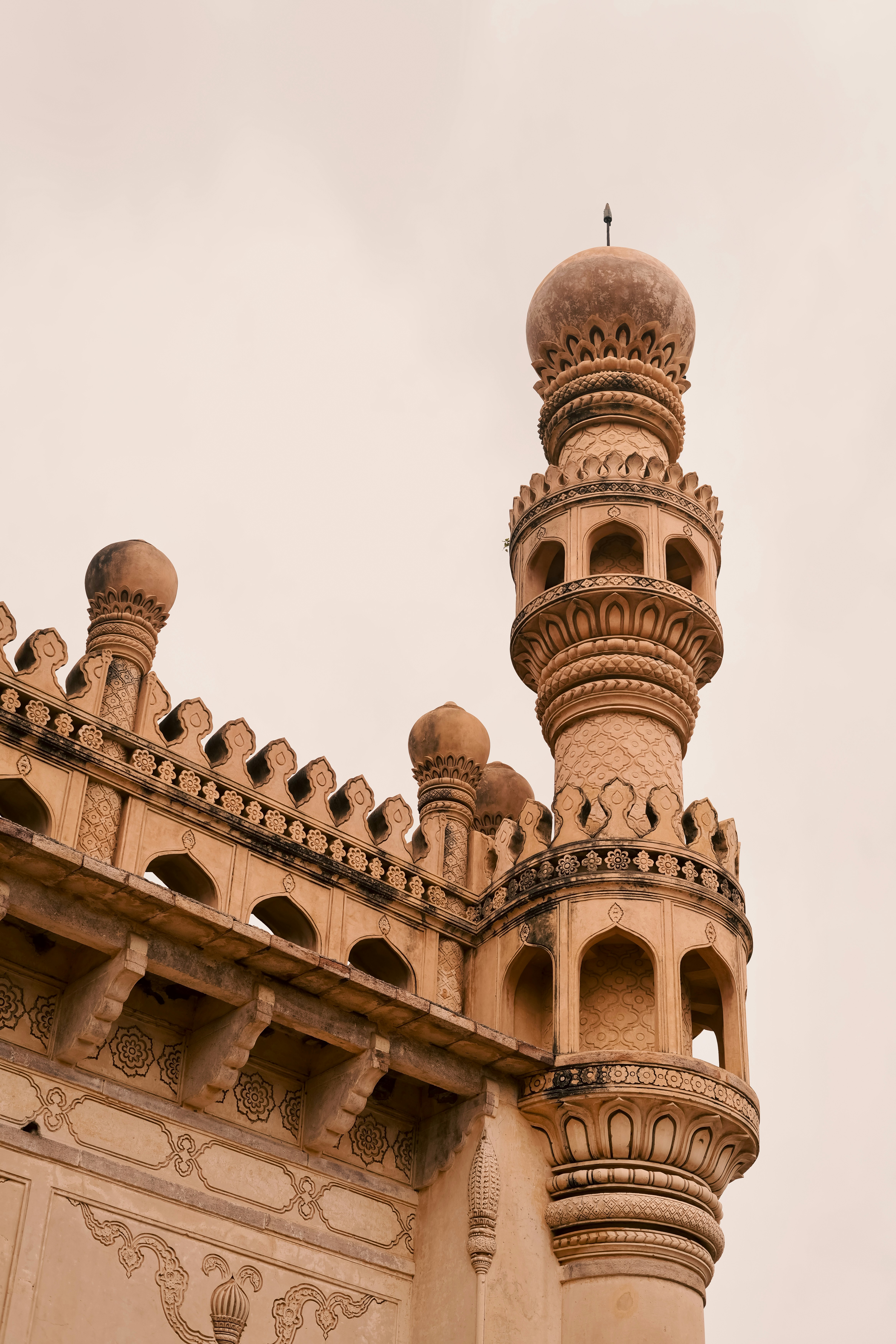 Intricately decorated minaret silhouette atop a carved courtyard wall, captured in warm sepia tones to emphasize architectural detail.
