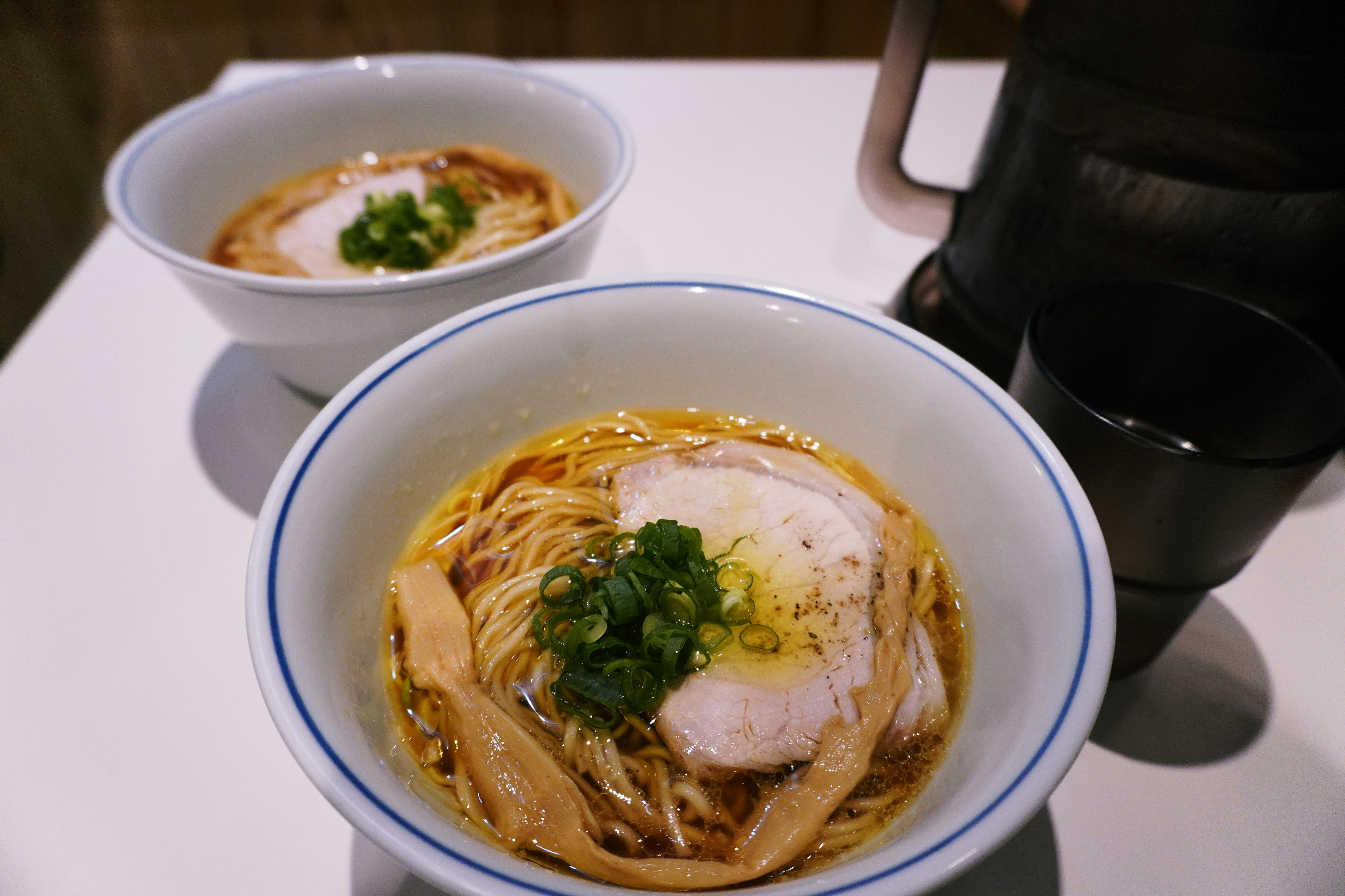 Bowl of savory noodles crowned with pork and greens on a minimalist table