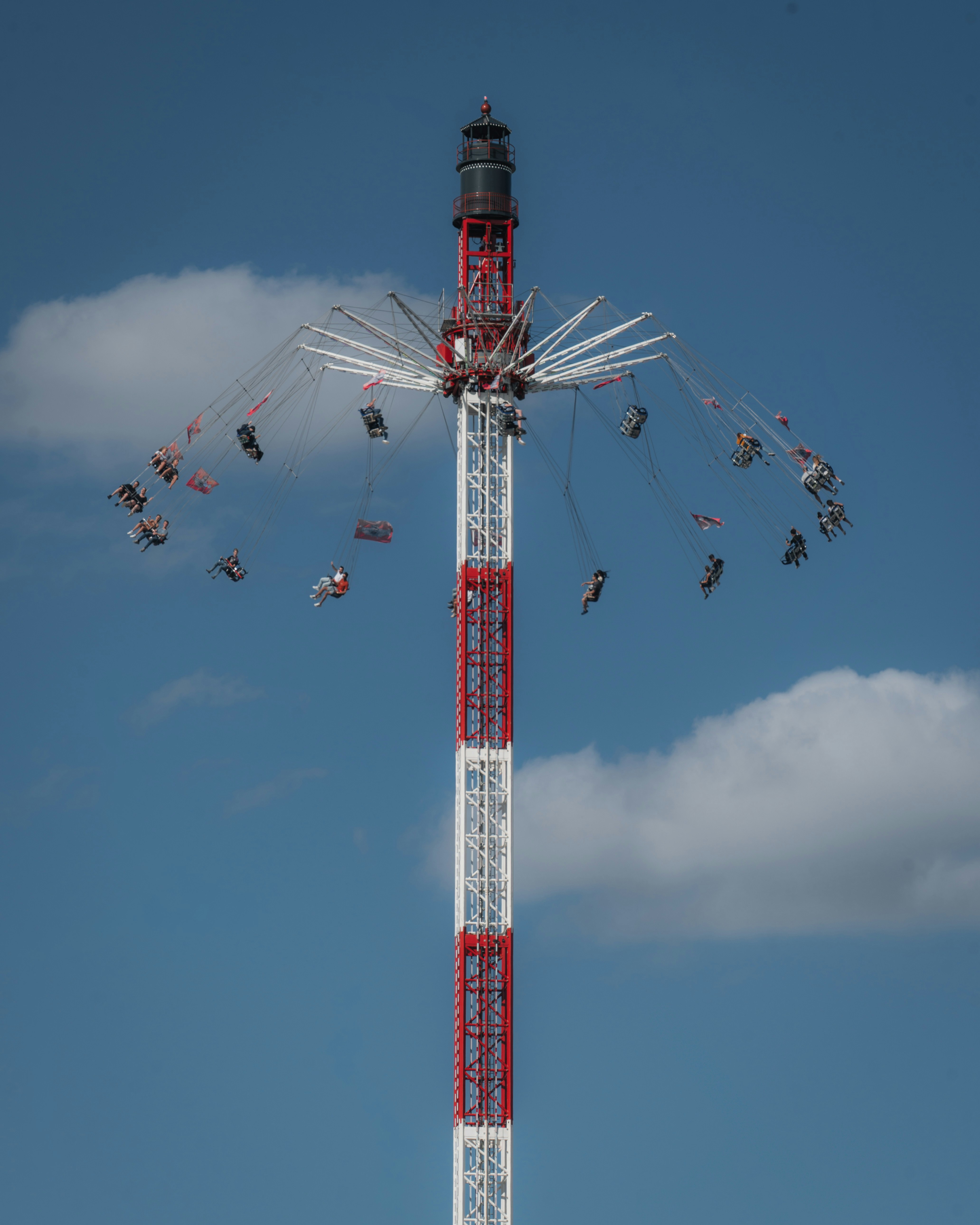 A towering red-and-white aerial ride with dozens of suspended seats circling from a central hub against a clear blue sky.
