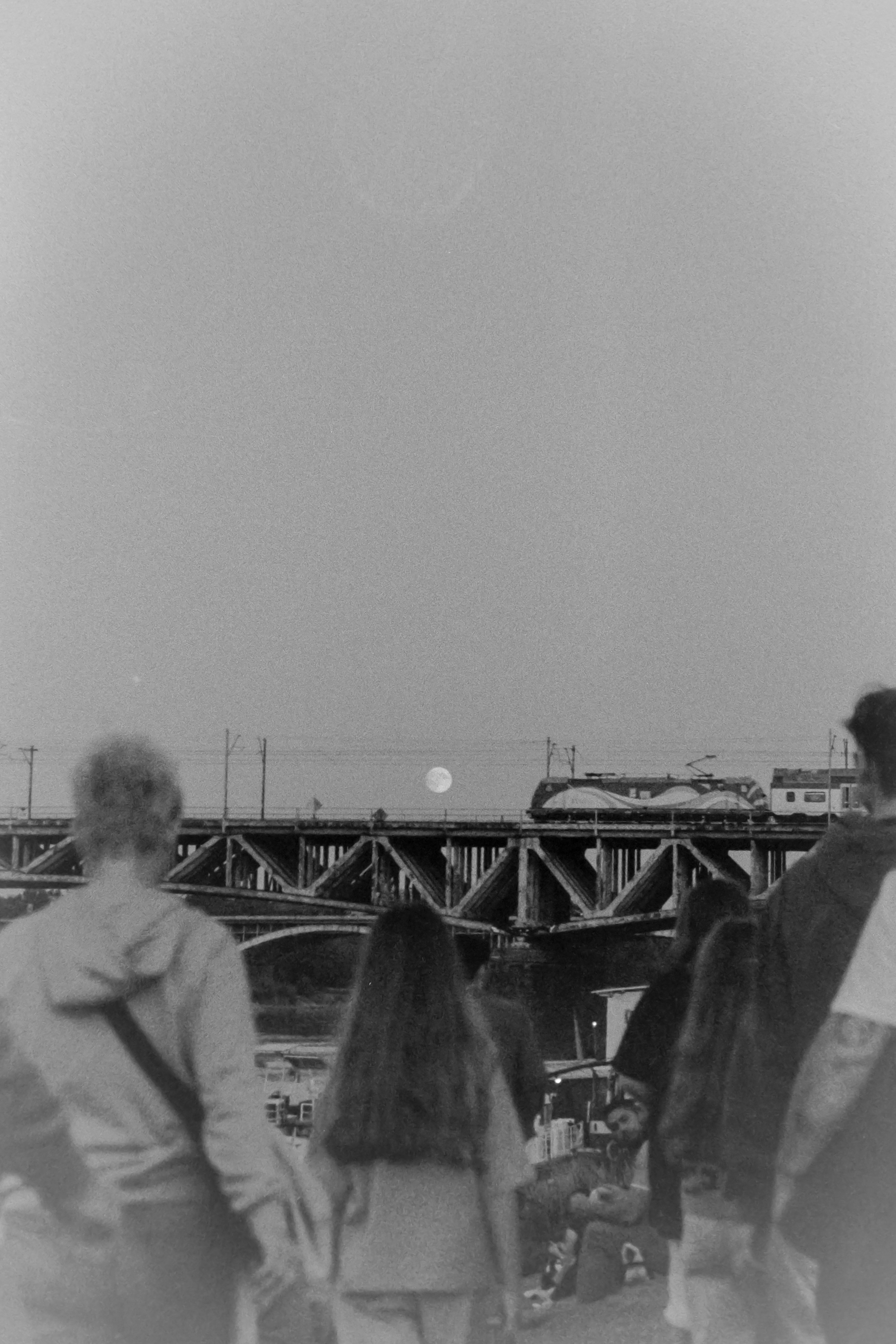 A group of people facing a train crossing a bridge under a full moon