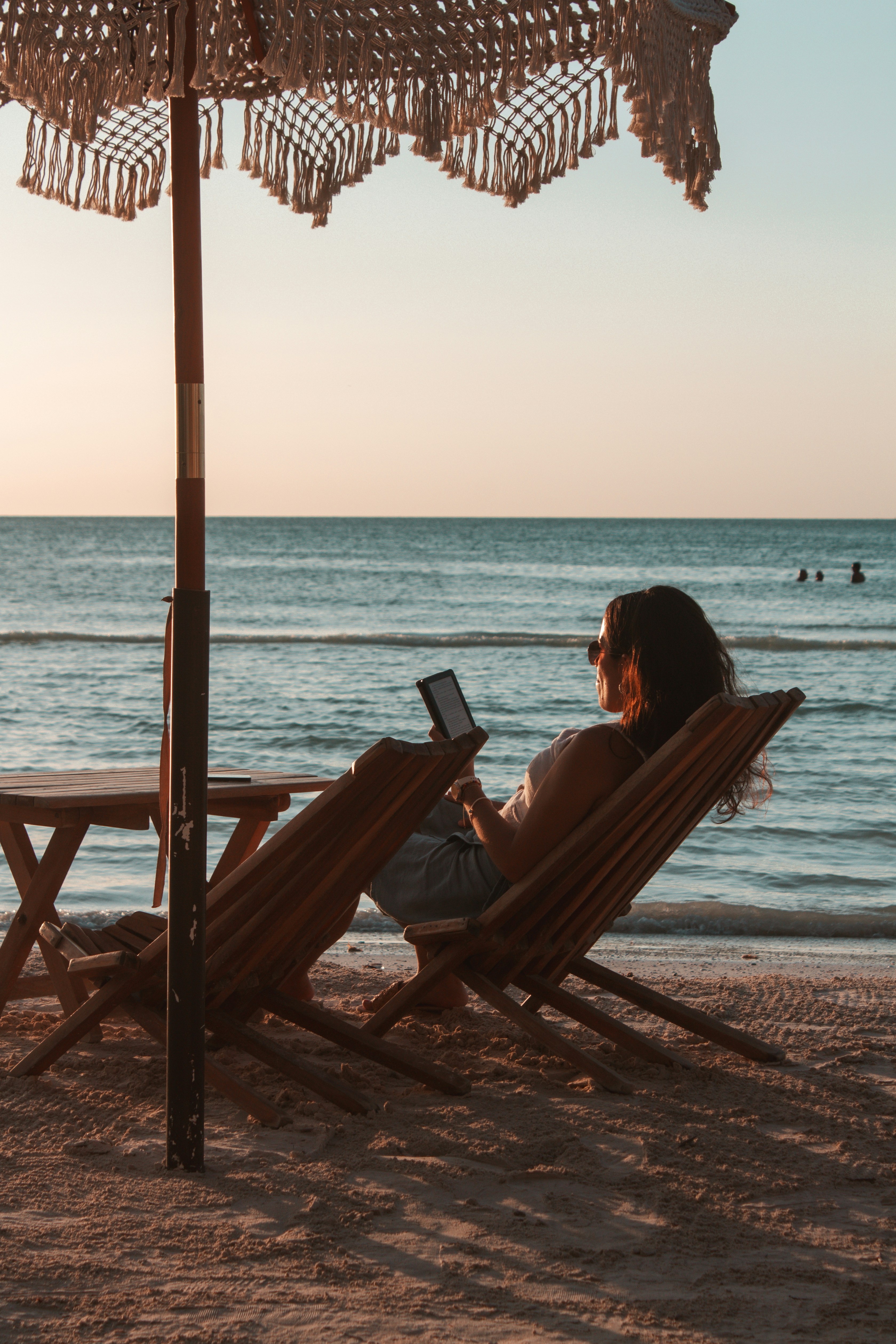 Sunset Leisure: A Woman Reclines with an E-Reader by the Sea