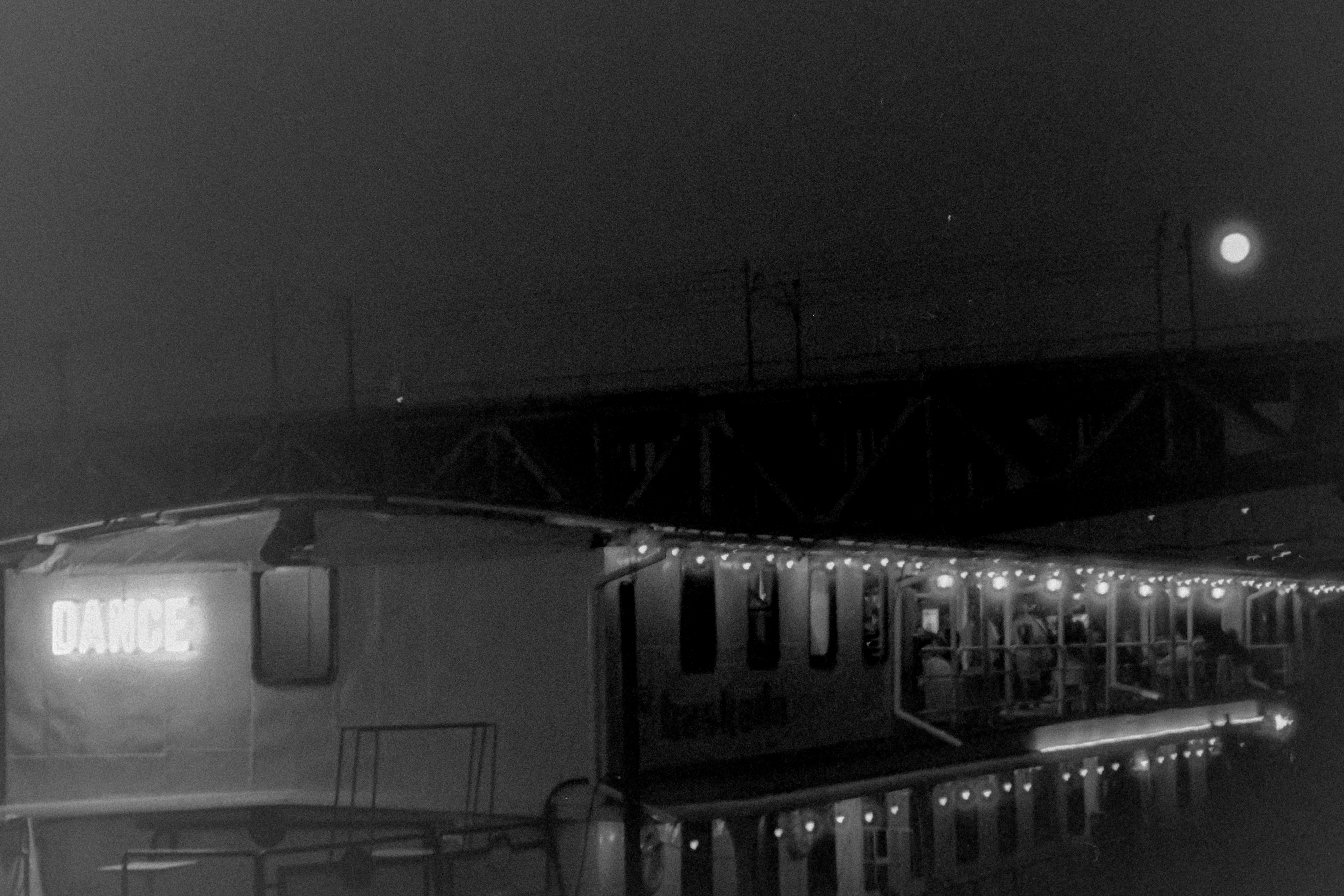 A black and white boat with a neon sign reading DANCE under a bridge