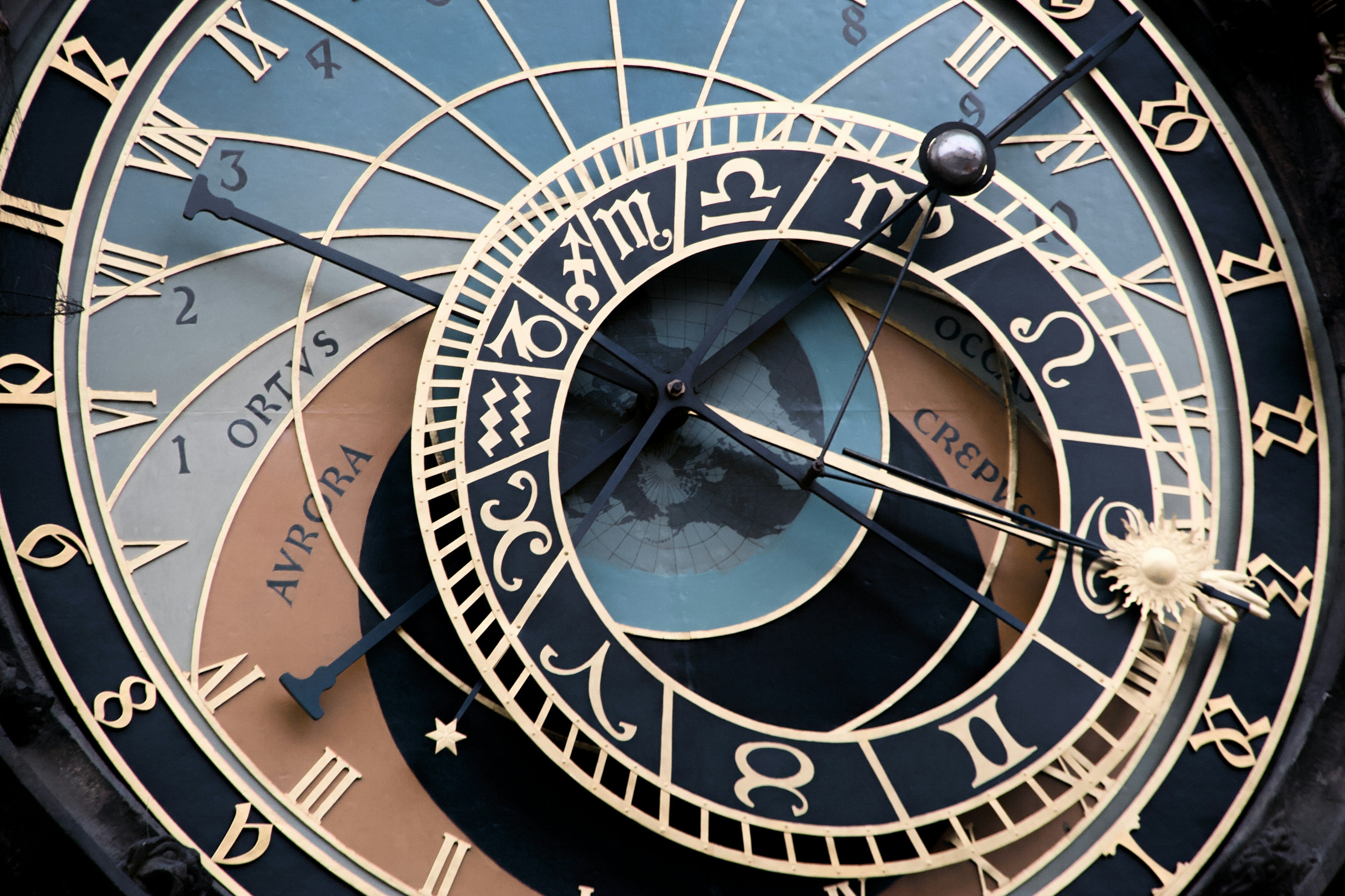 Close-up of an ornate astronomical clock with concentric rings and zodiac glyphs, highlighting gears and hands in a decorative, historical centerpiece.
