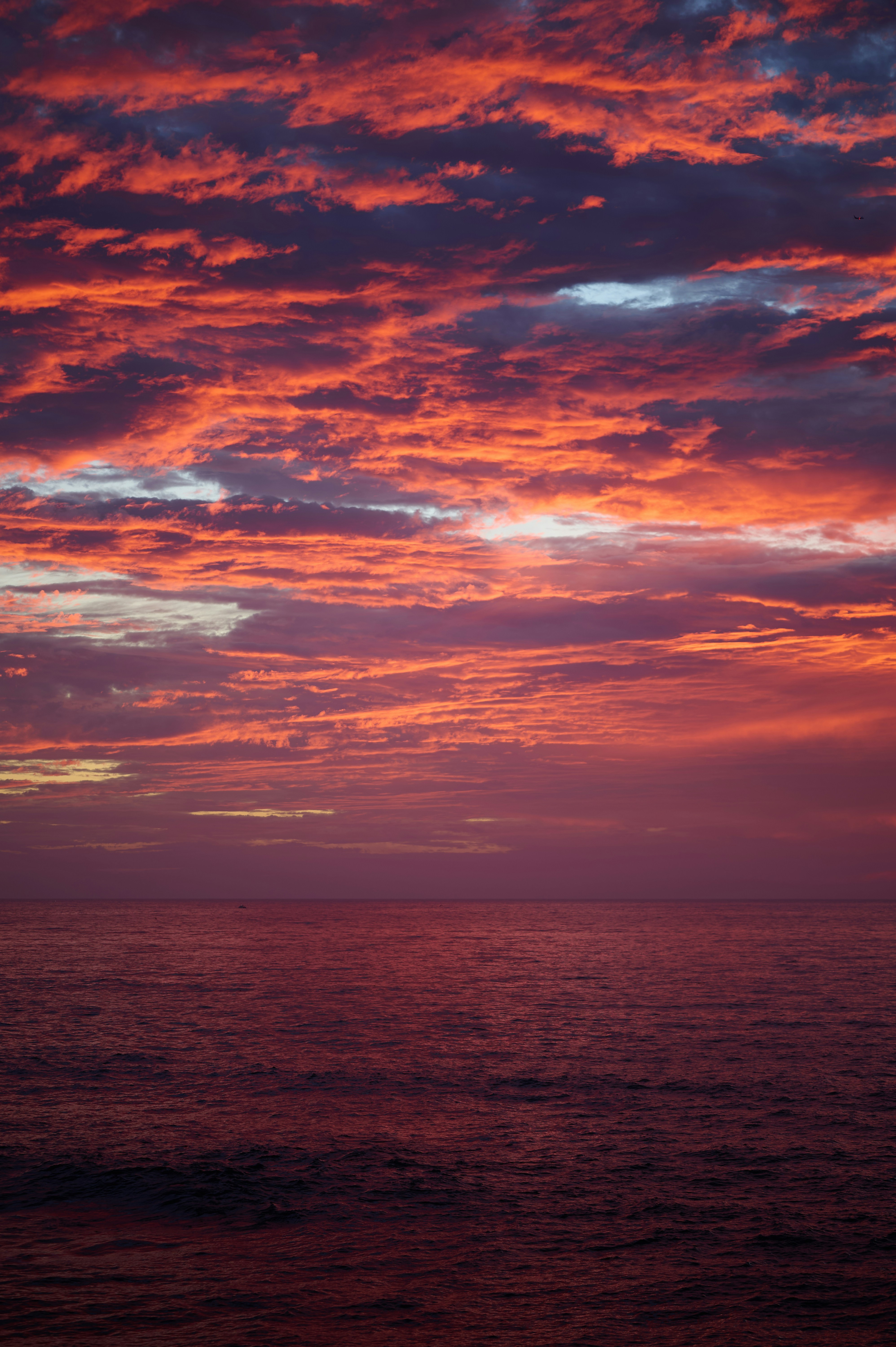Vibrant sunset over a calm sea with dramatic orange and purple clouds stretching across the sky.