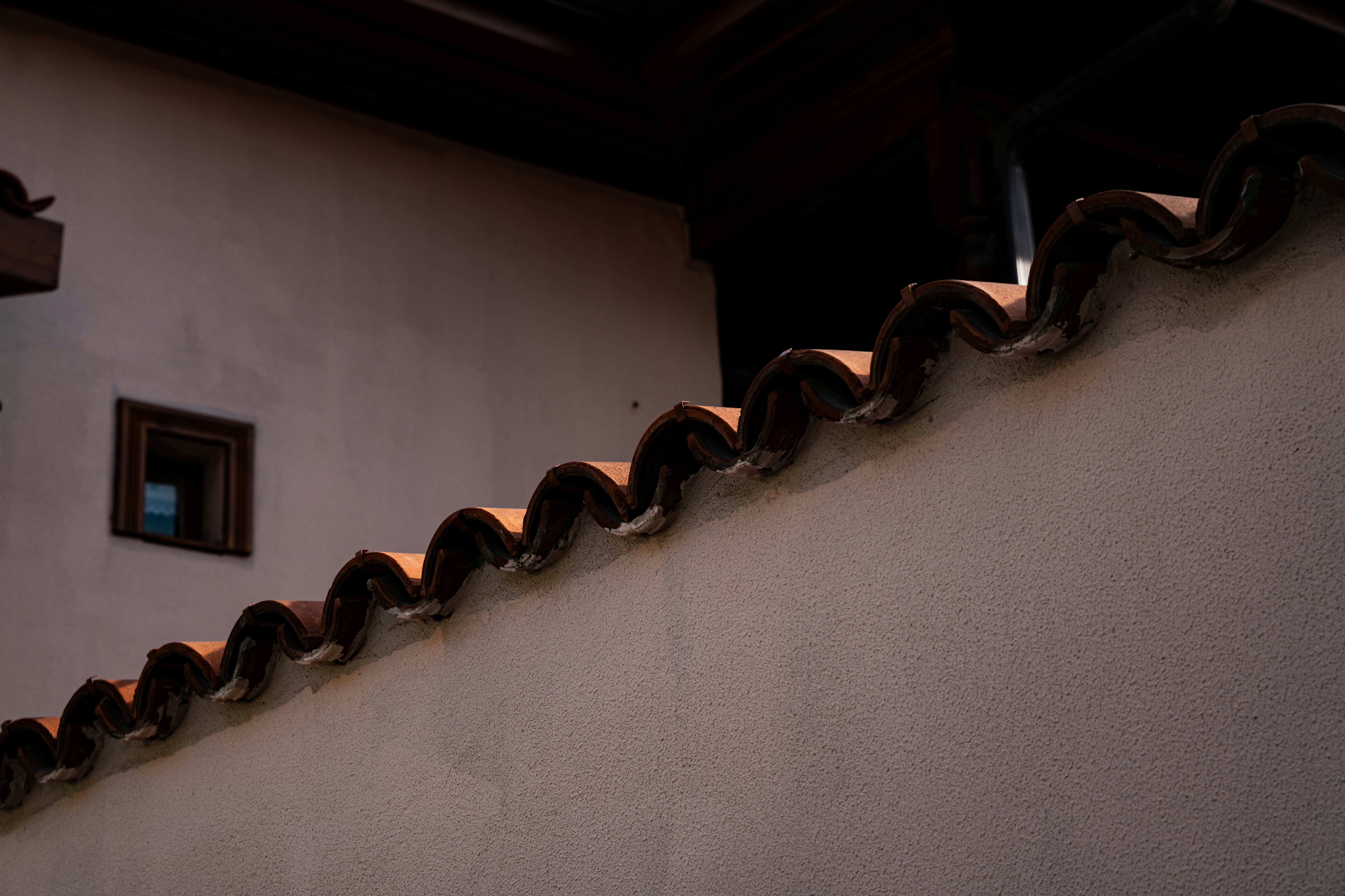 A curved terracotta tile roof edge against a plain white wall with a window