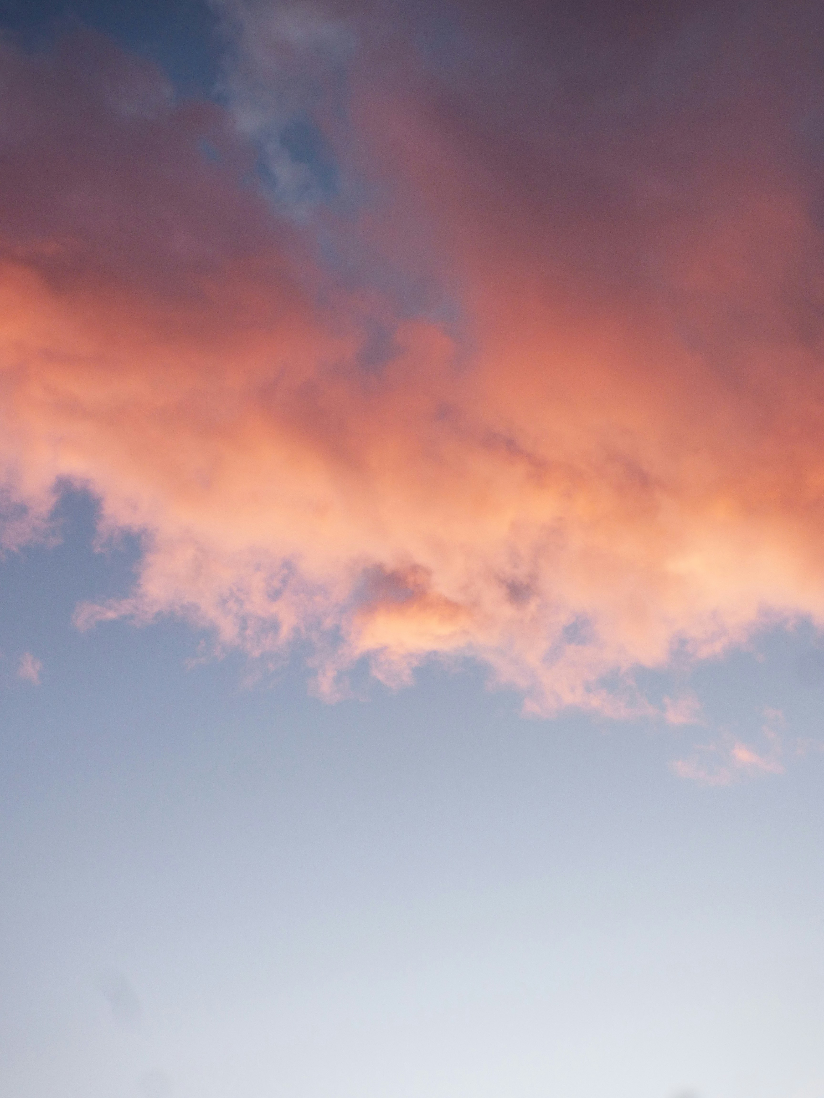 Pink-tinged cloud bank drifting over a pale horizon