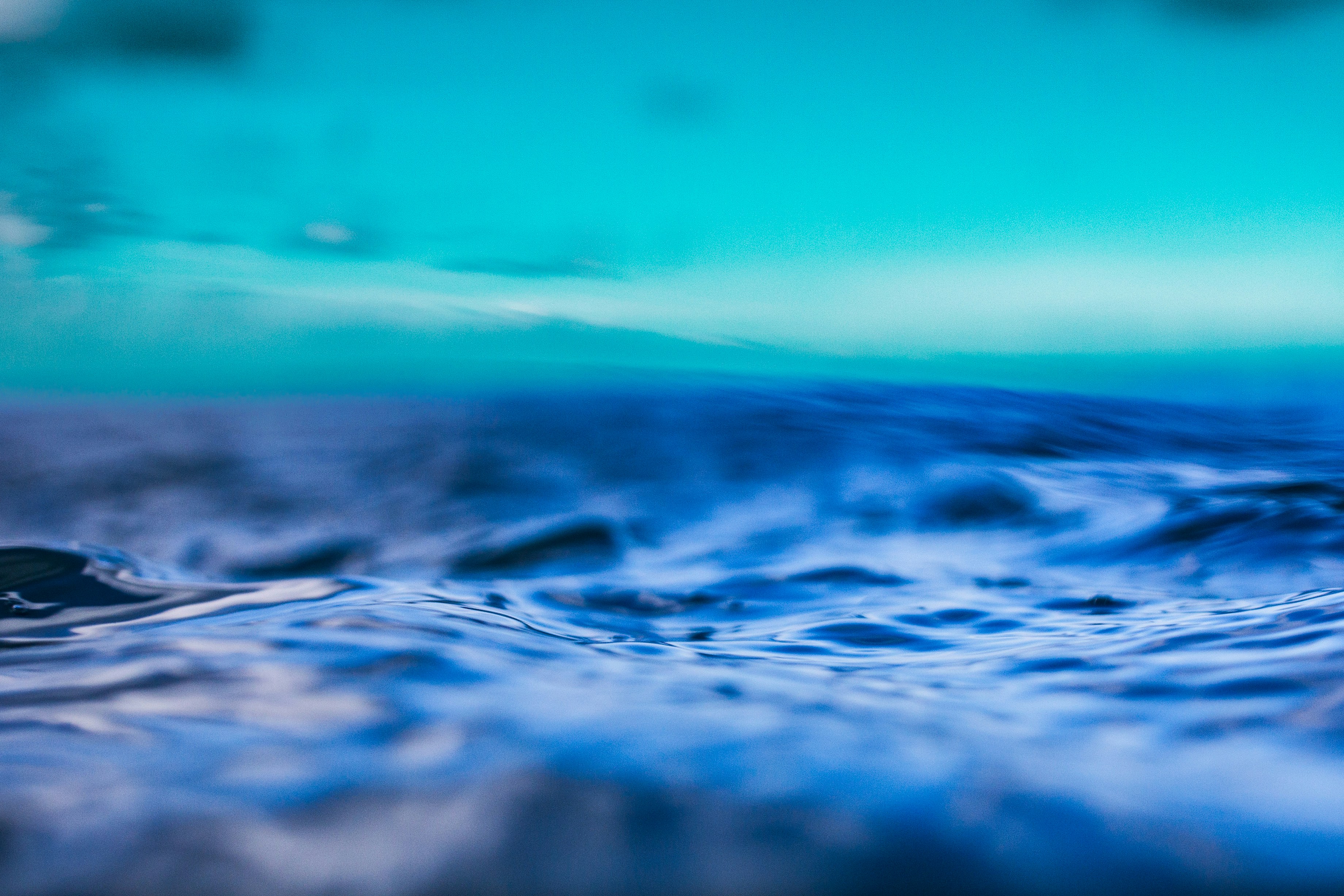 Blue-toned sea surface with a soft, blurred horizon and cyan sky, emphasizing smooth gradients and gentle motion without a distinct subject. A minimalist aquatic abstract suitable for a calming ambient mood.
