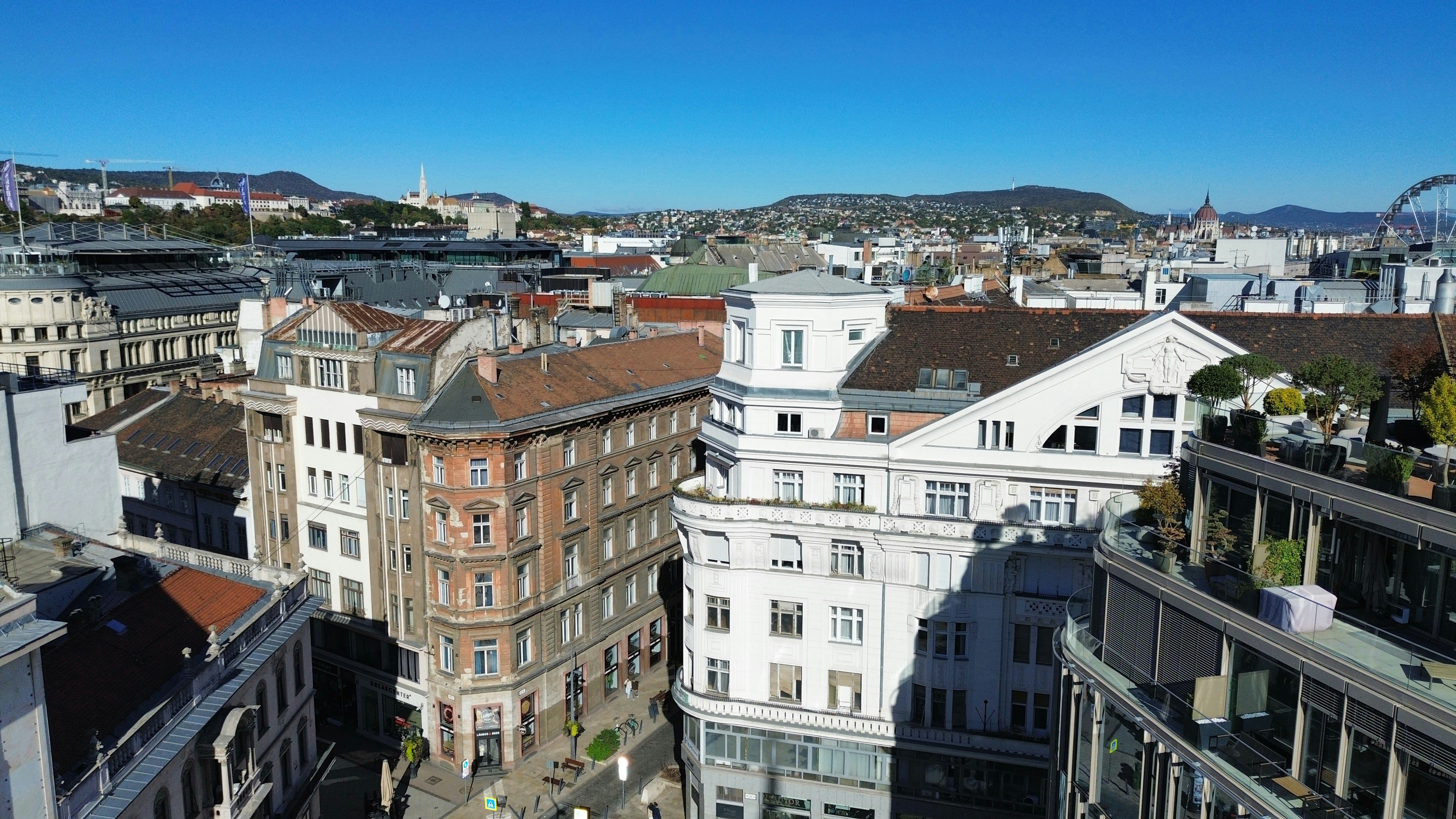Aerial Morning over a Rooftop Arc: Facades and Distant Ferris Wheel
