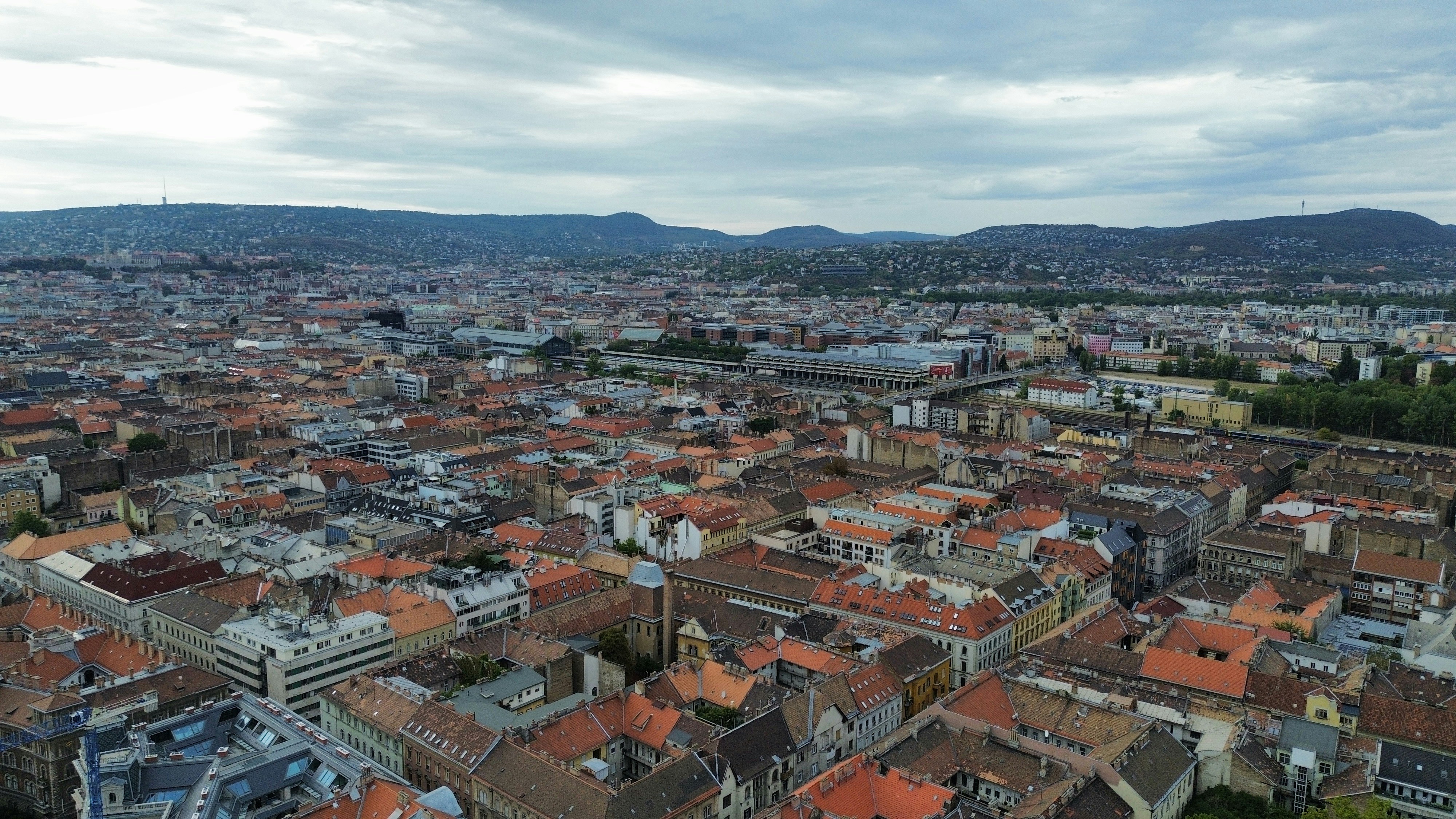 Aerial view of a dense European city with red-tiled roofs and a patchwork of streets beneath a cloudy sky.