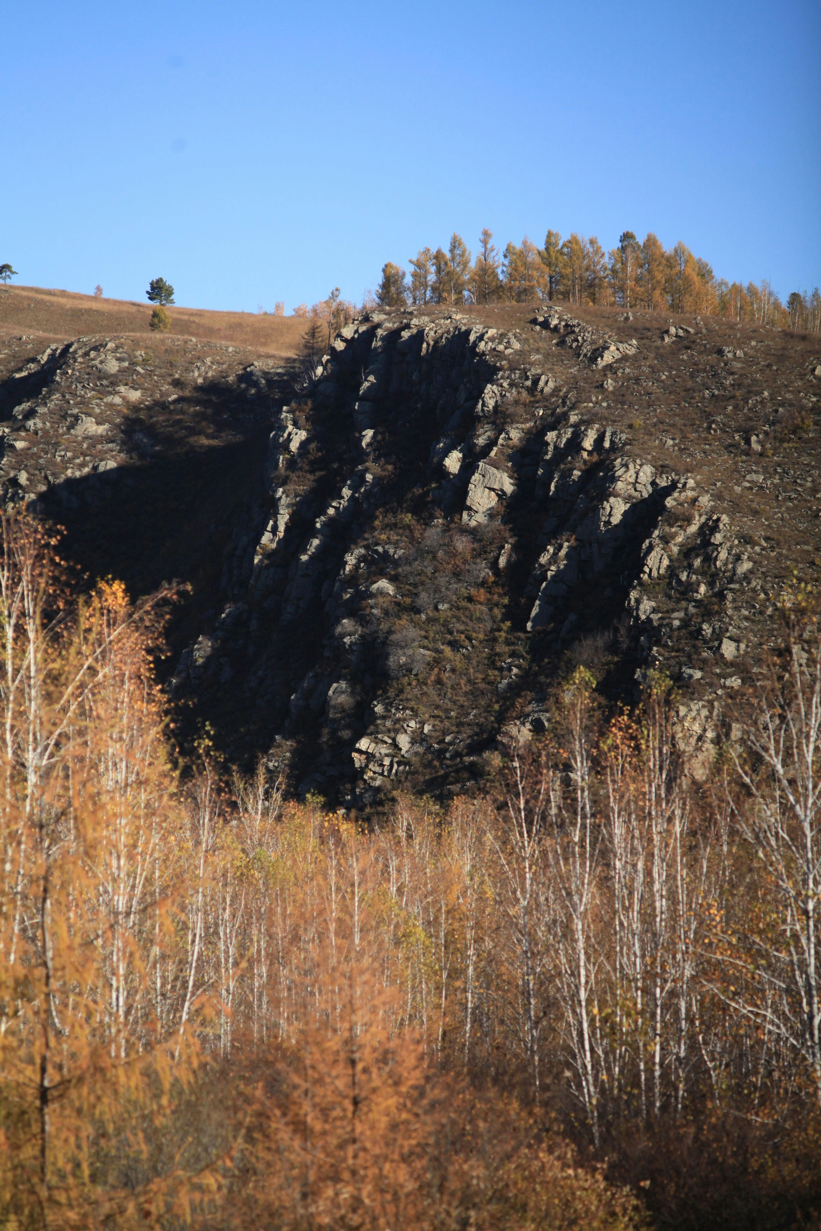 Sunlit Ridge and rugged cliff Amid Autumn Forest
