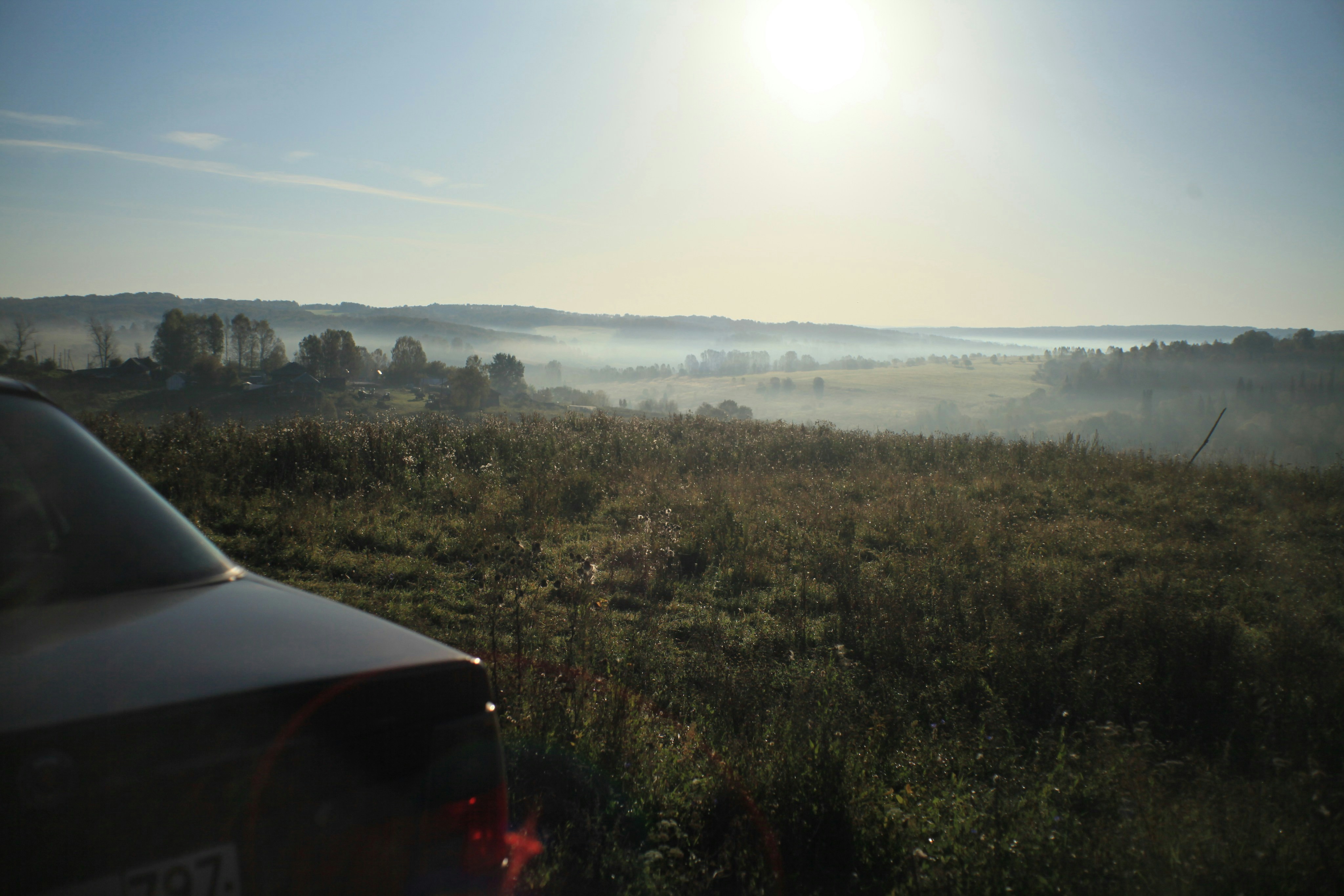 Dawn over Mist-Kissed Field with Car Silhouette