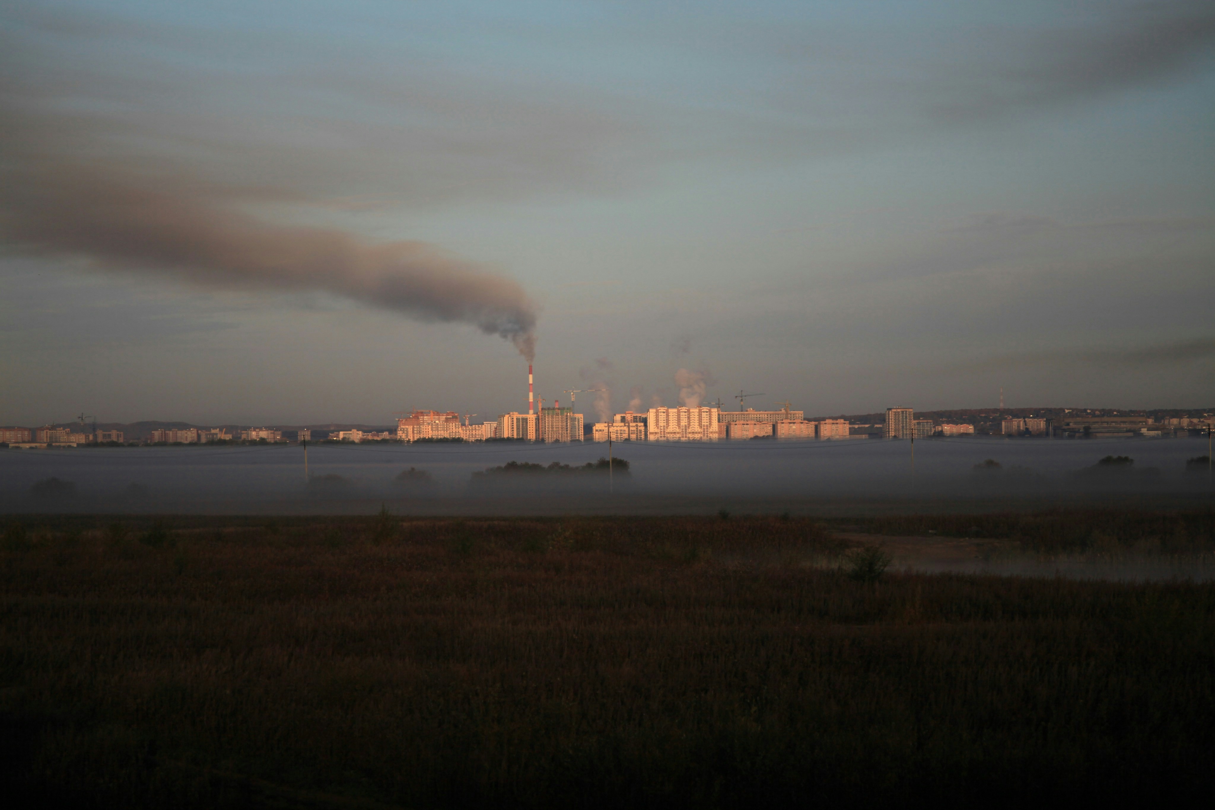 Industrial skyline at dawn: a distant plume over a fog-kissed river belt