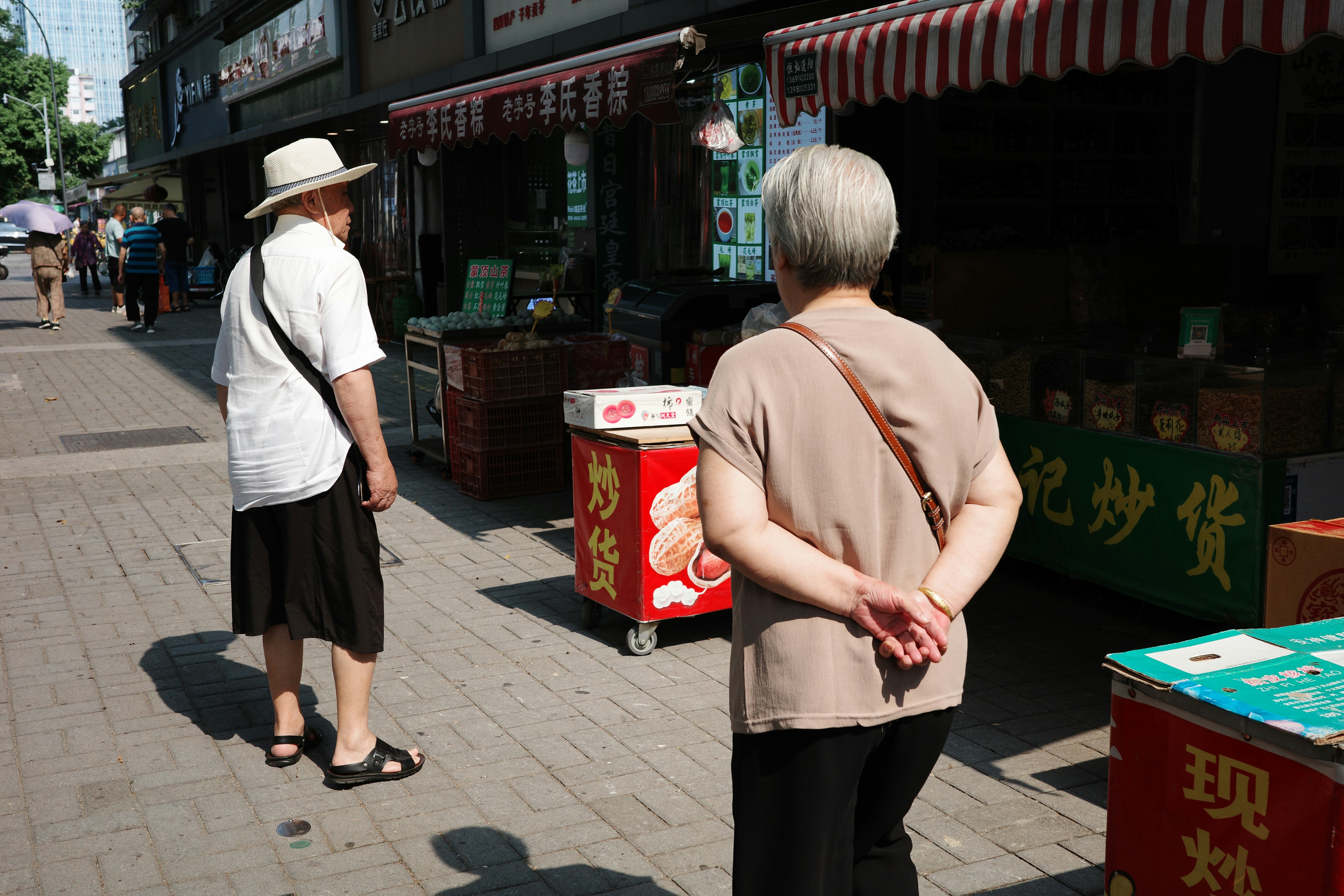 Two Passersby in a Sunlit Market Corridor