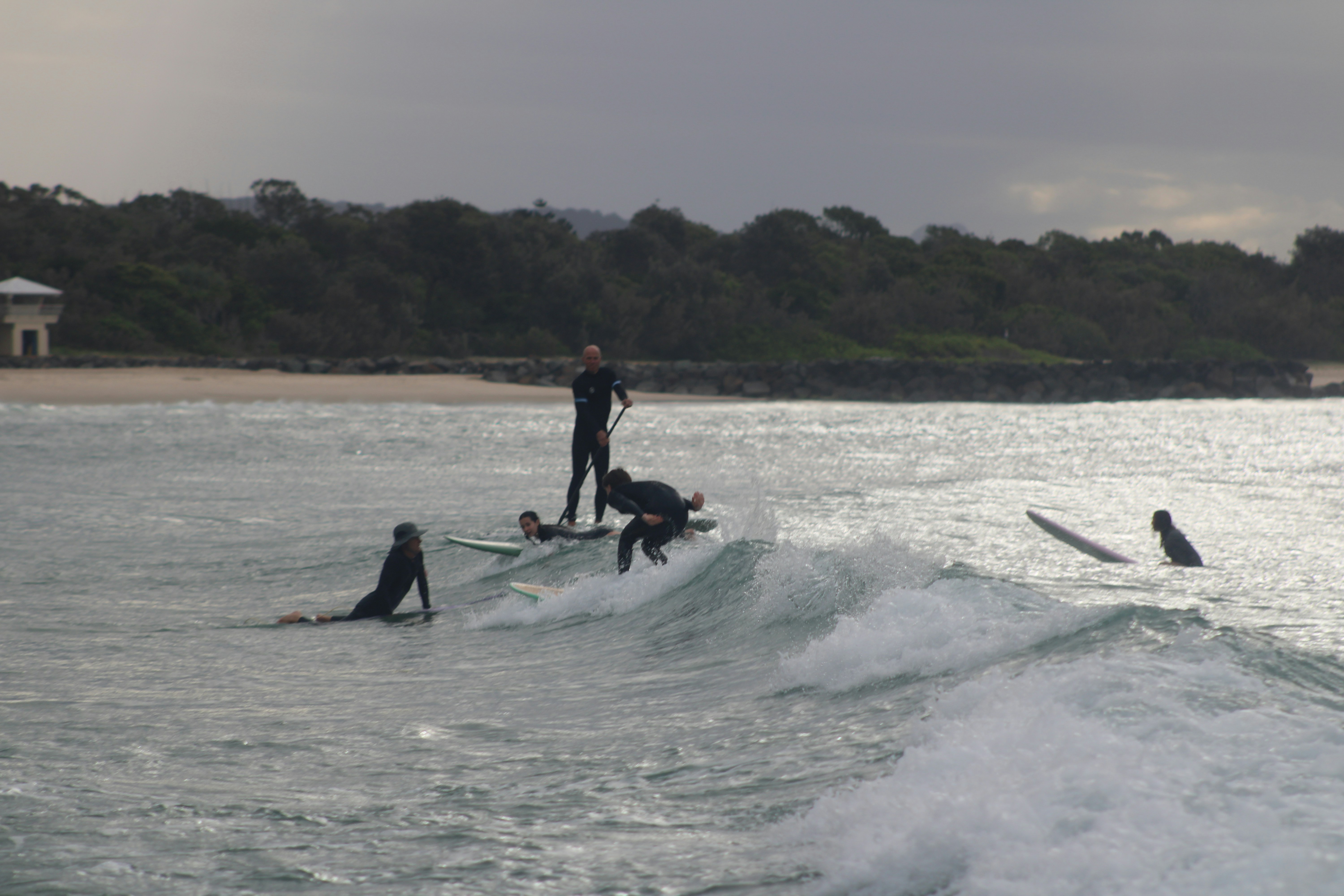 Surfing crew rides a curling wave under a gray seaside sky