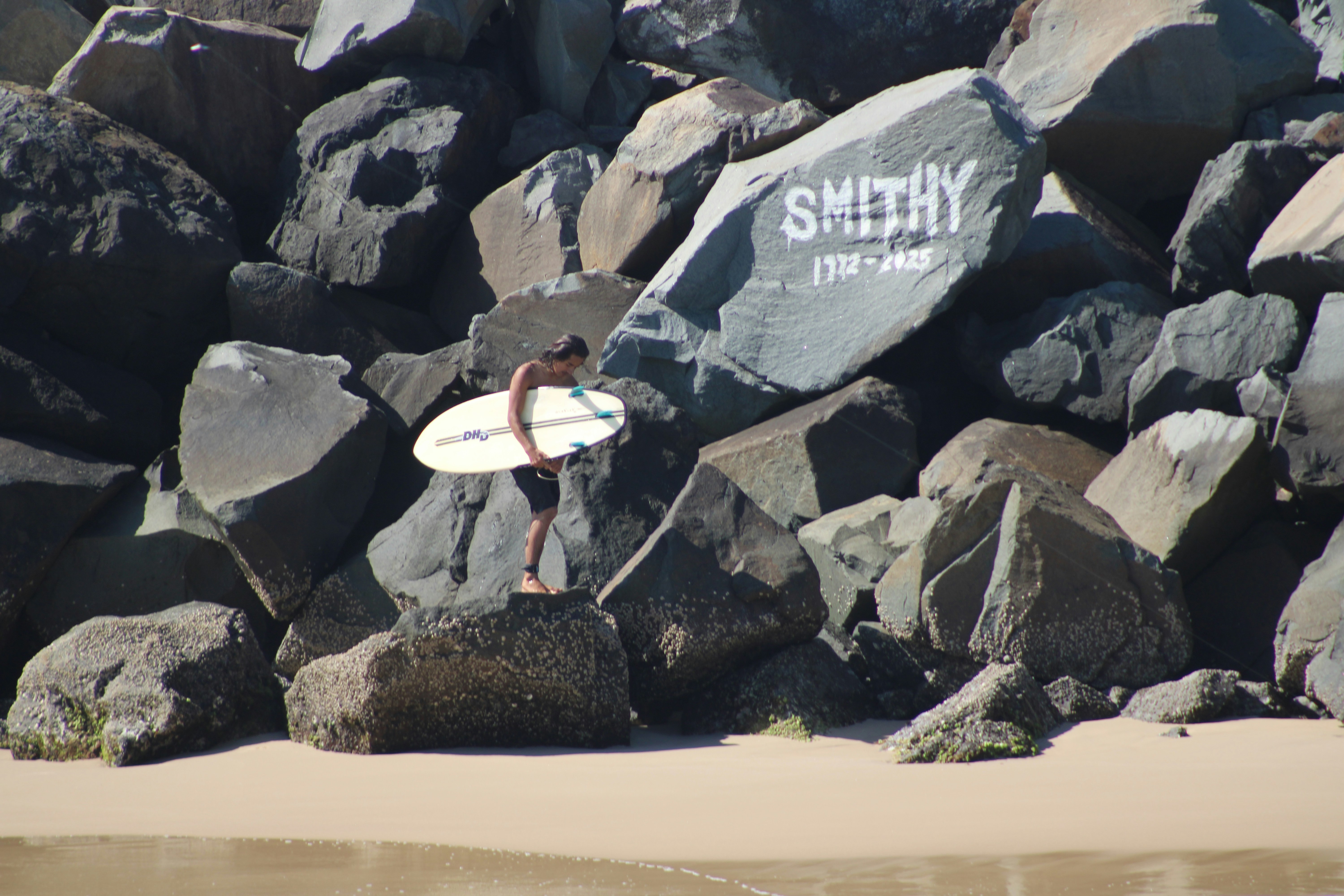 Riding the Tide: Surfer Navigates a Boulder Break on a Quiet Beach