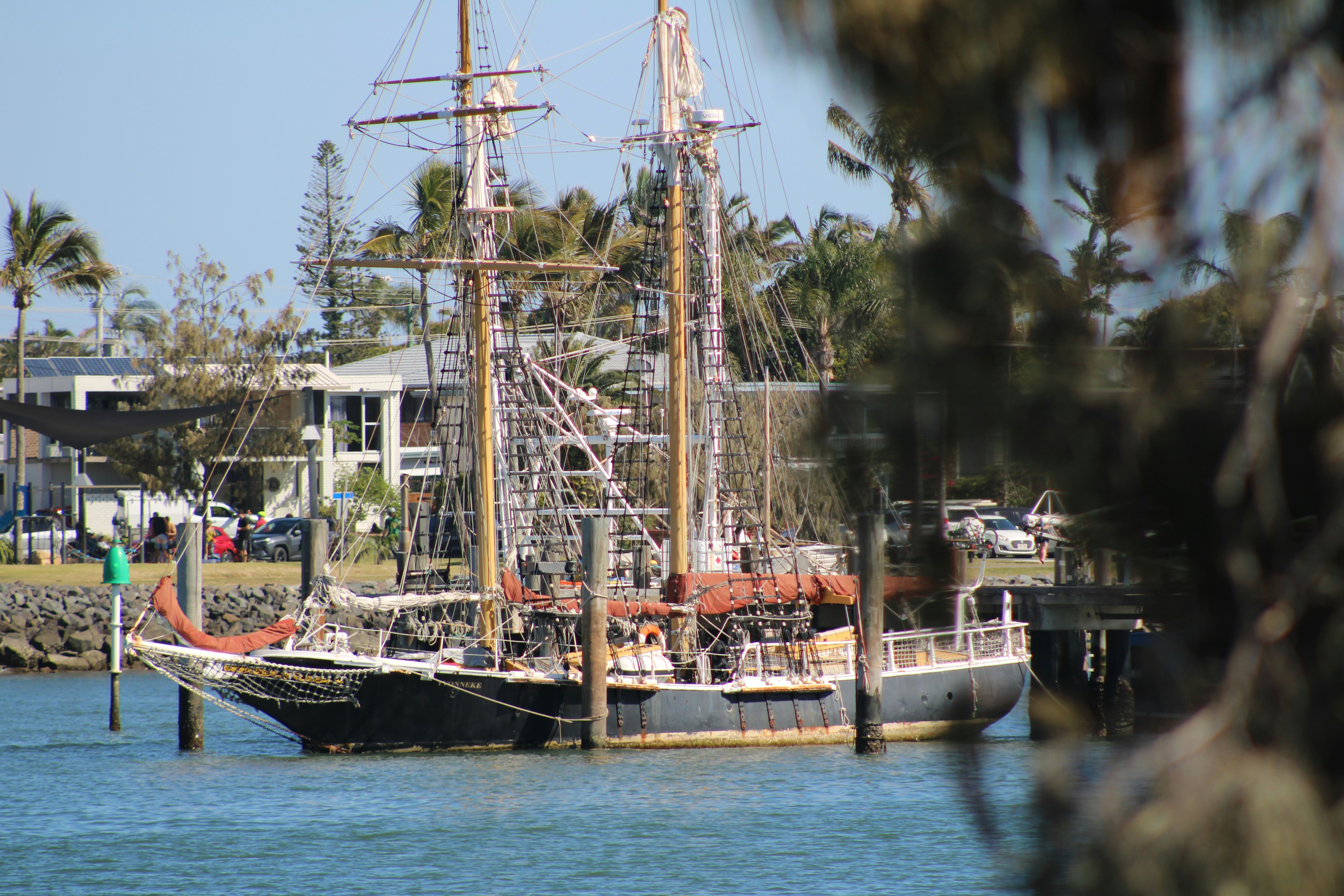 Masted Vessel at Docks: A Quiet Harbor Scene Framed by Looming Foliage