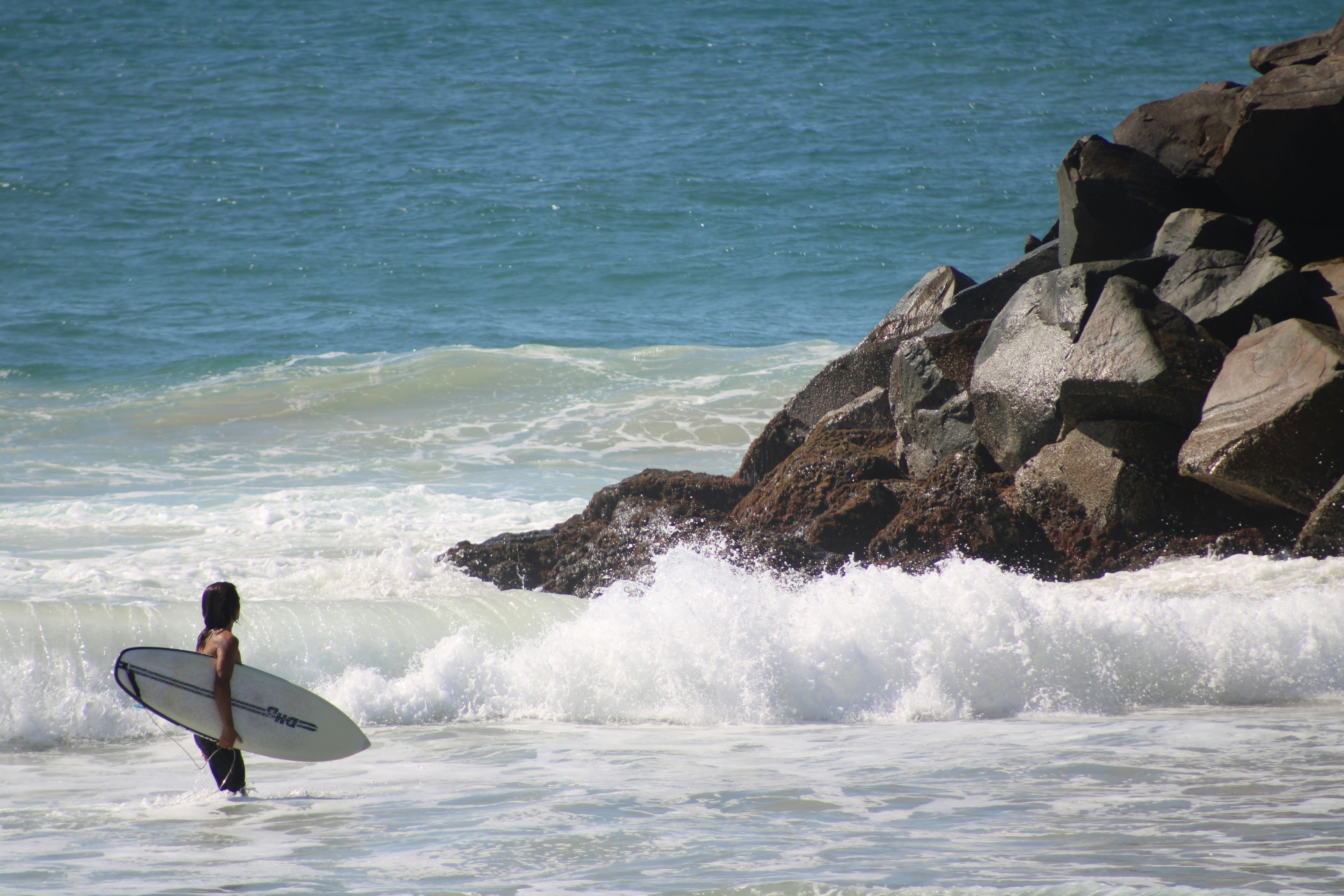 Surfer Returns to Shore: a lone rider navigates a frothy exit past rocky breakwater