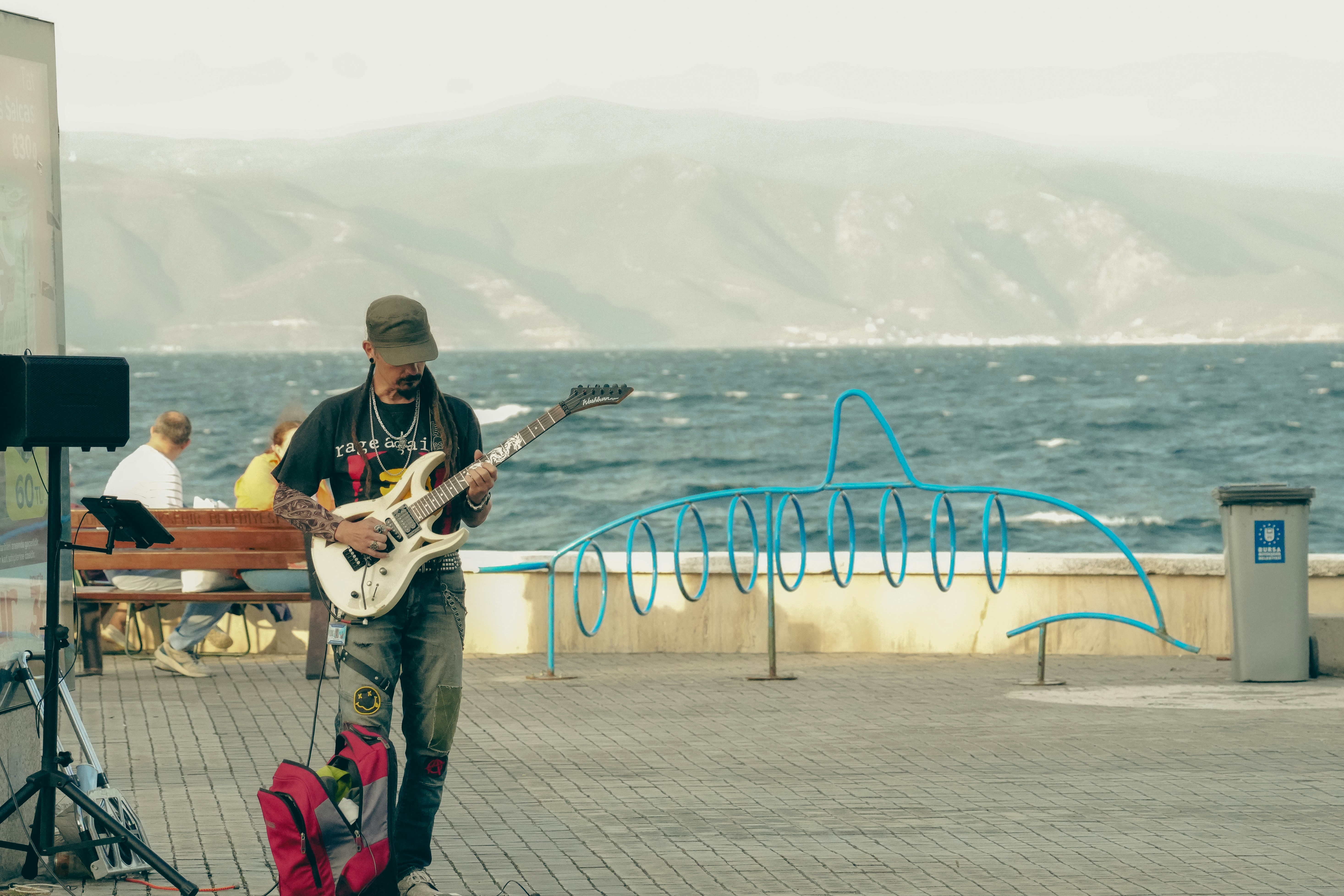 Street musician in coastal plaza: guitar riffs by the rail