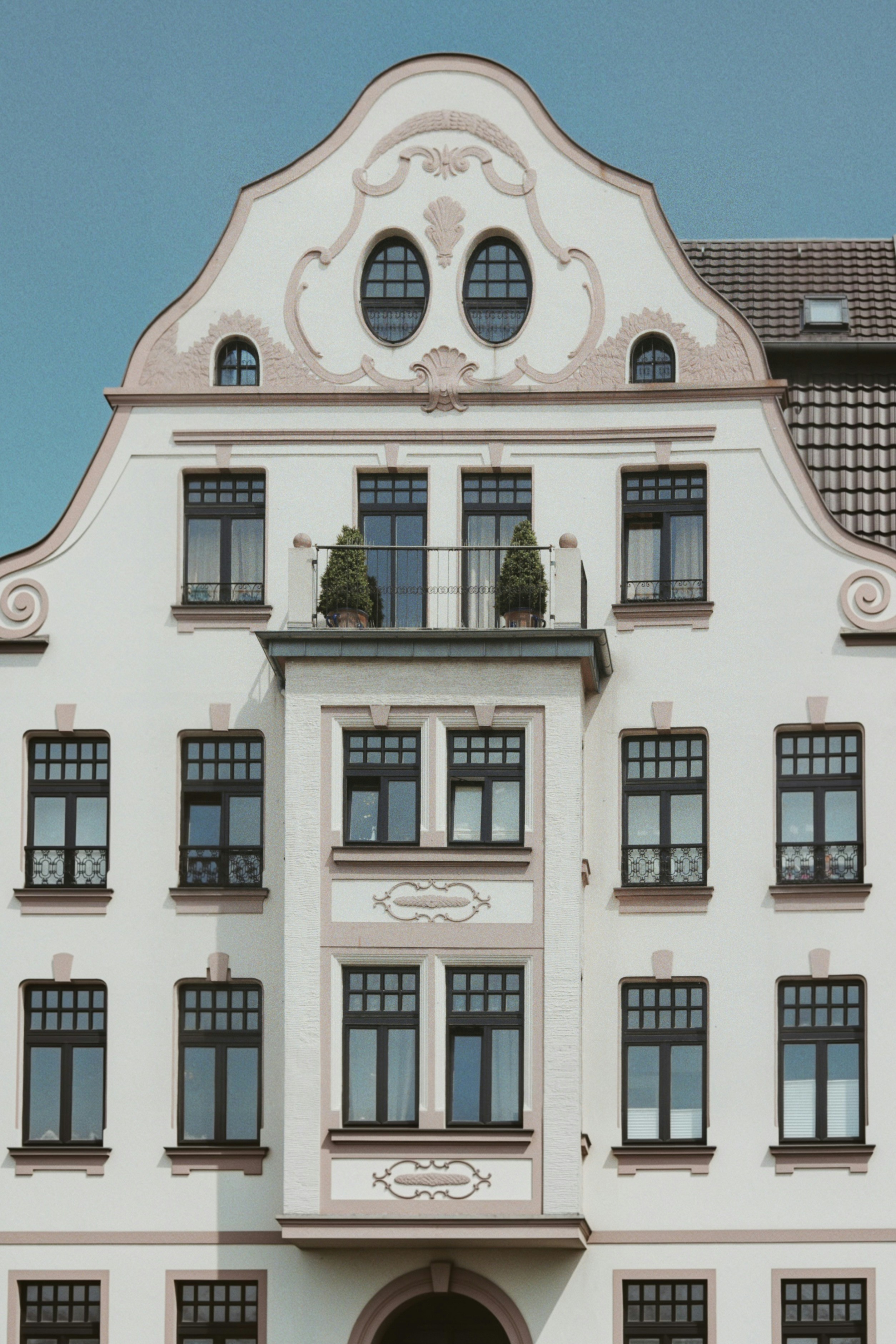 Sculpted white facade with arched windows and a central balcony, showcasing decorative molding and symmetry; a classic European residential building.
