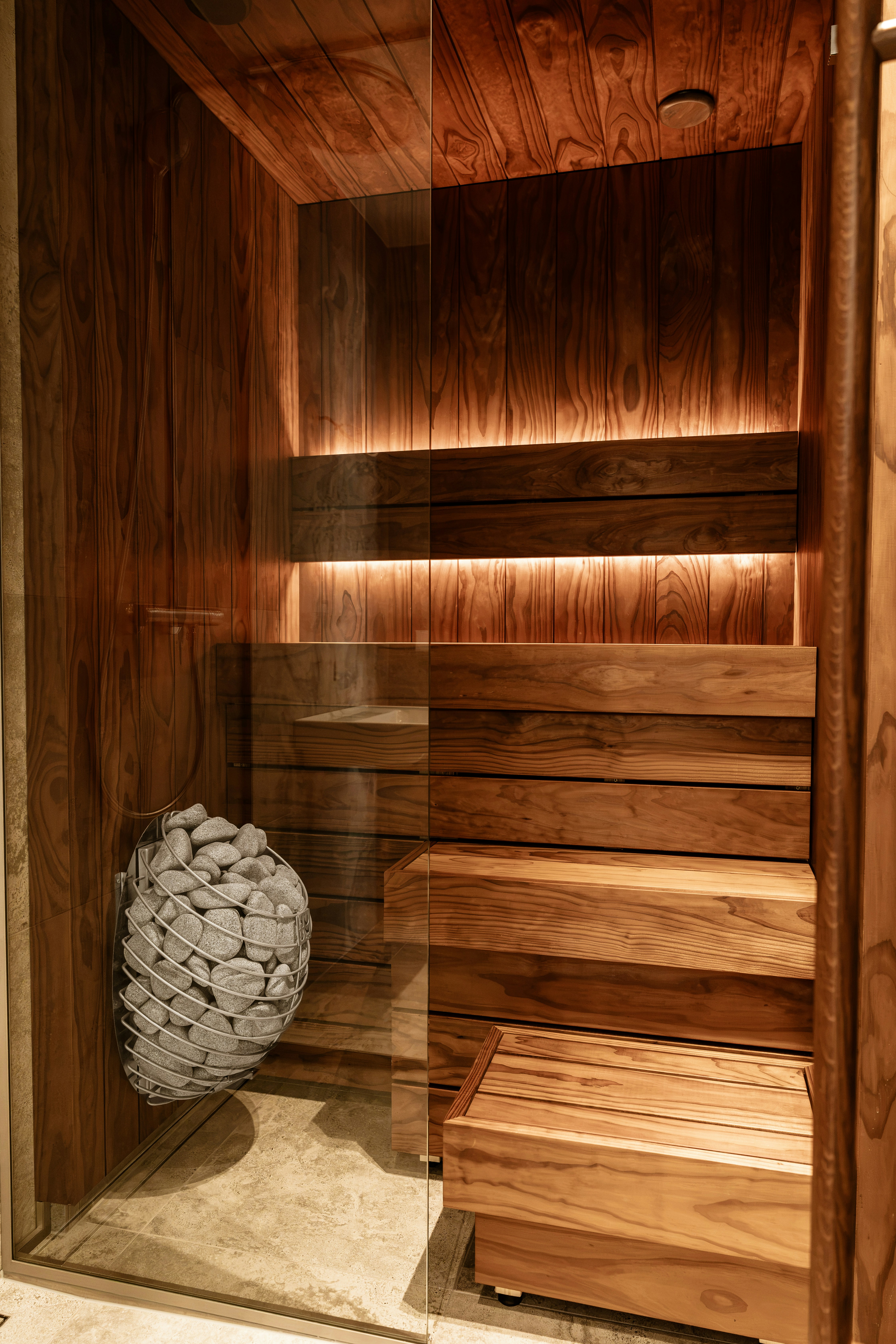 Quiet sauna chamber with woven stone heater tucked in a glass-walled nook