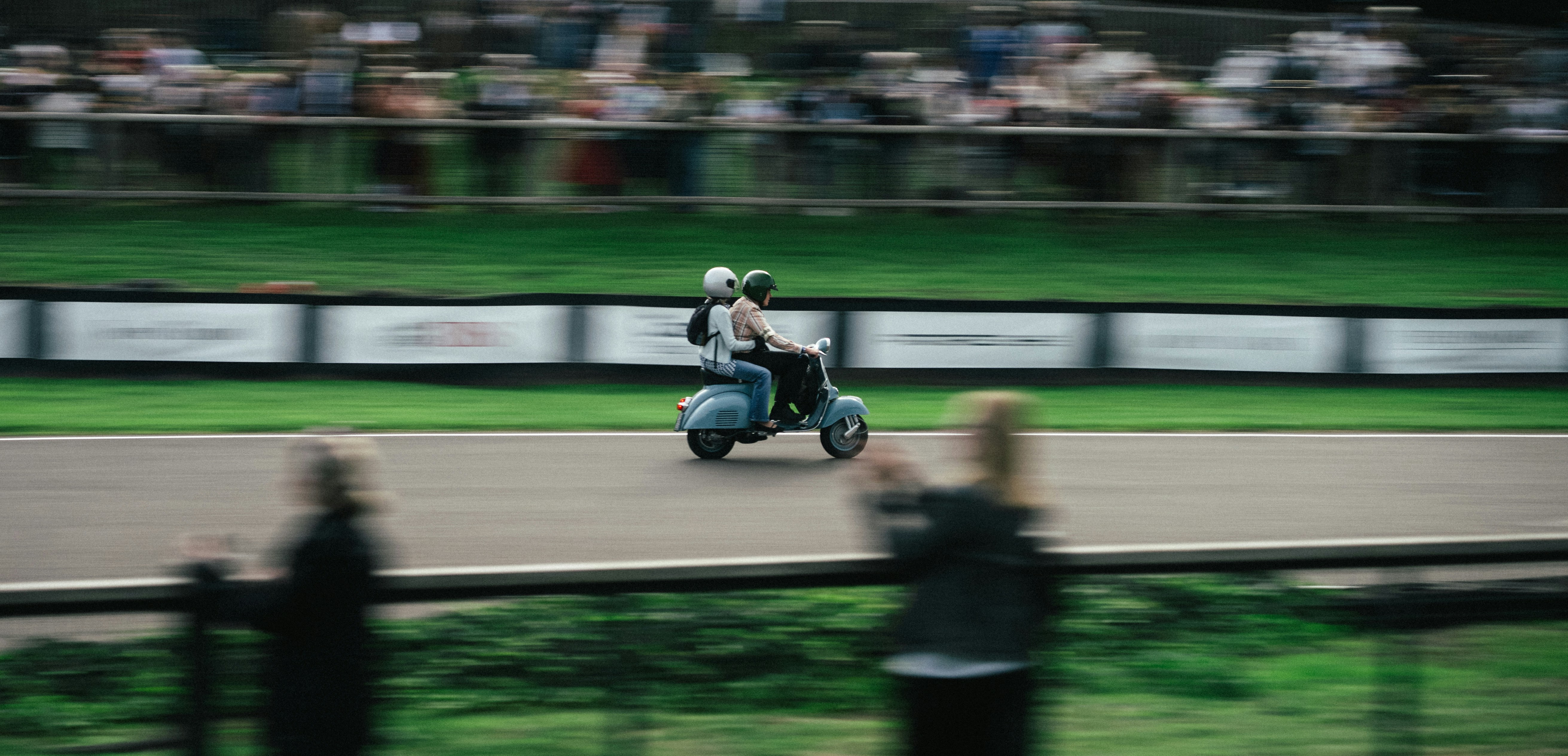 Tiny Blue Scooter in Motion: Riders on a Blur of Green and Trackside Fans