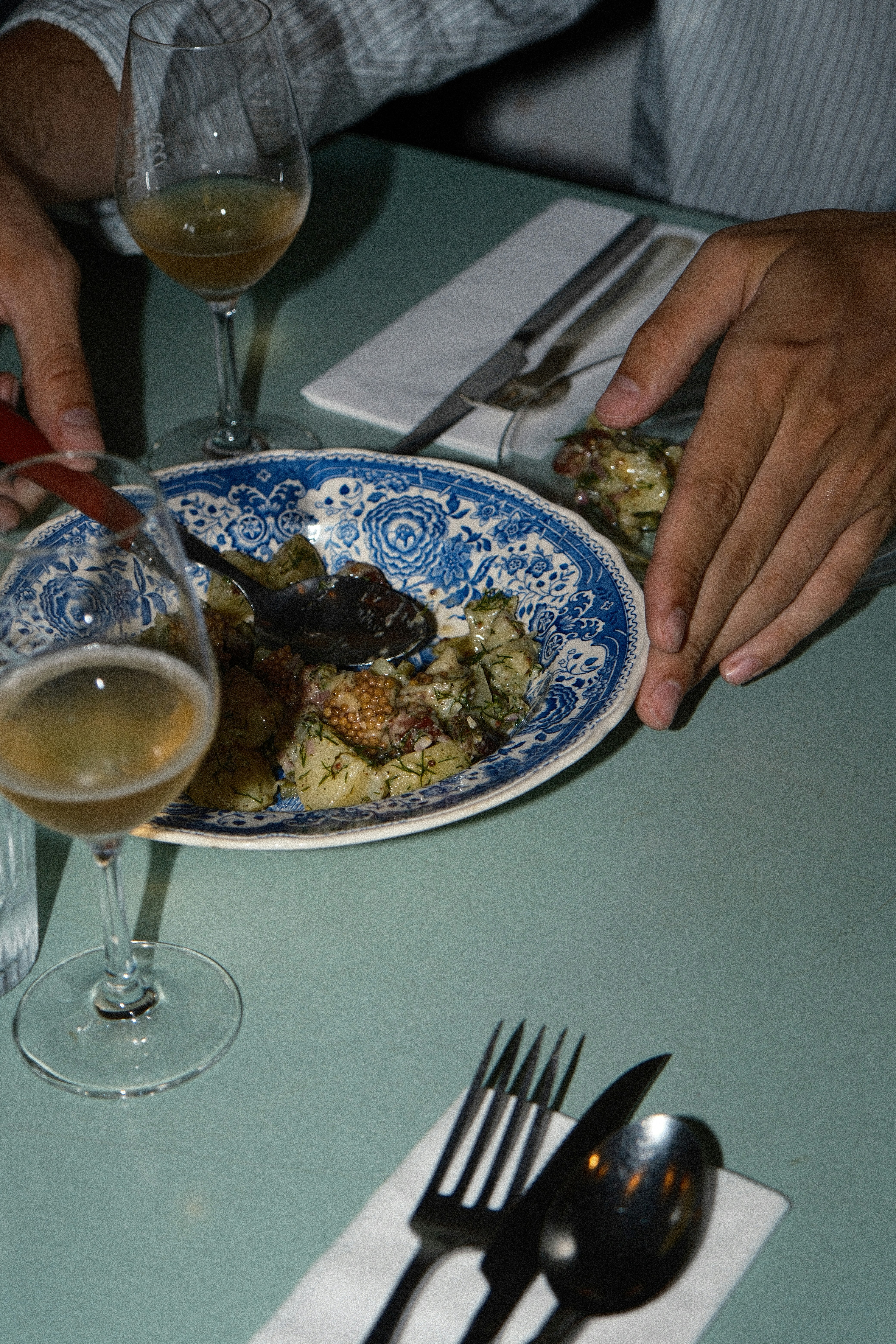 Shared Plate, Quiet Toast: A Dining Moment Framed by Glassware and Hands