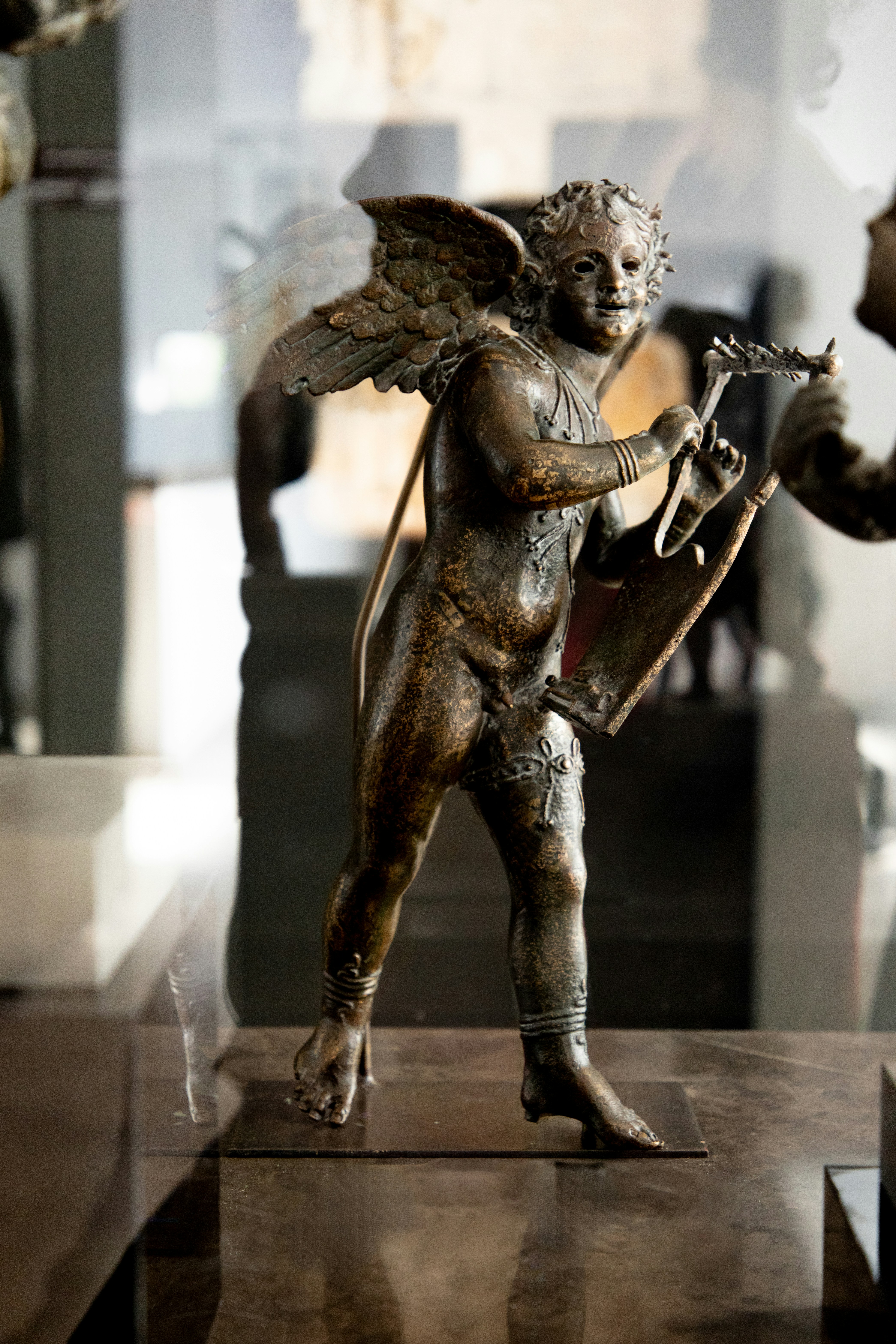 A detailed shot of a Hellenistic bronze statuette representing winged Eros (Cupid) playing the lyre or cithara. This remarkable artwork, featuring intricate details on the wings and dynamic posture, originates from the famous ancient Greek cargo recovered from the Mahdia Shipwreck (1st century BC) and is housed at the Bardo Museum in Tunis.
