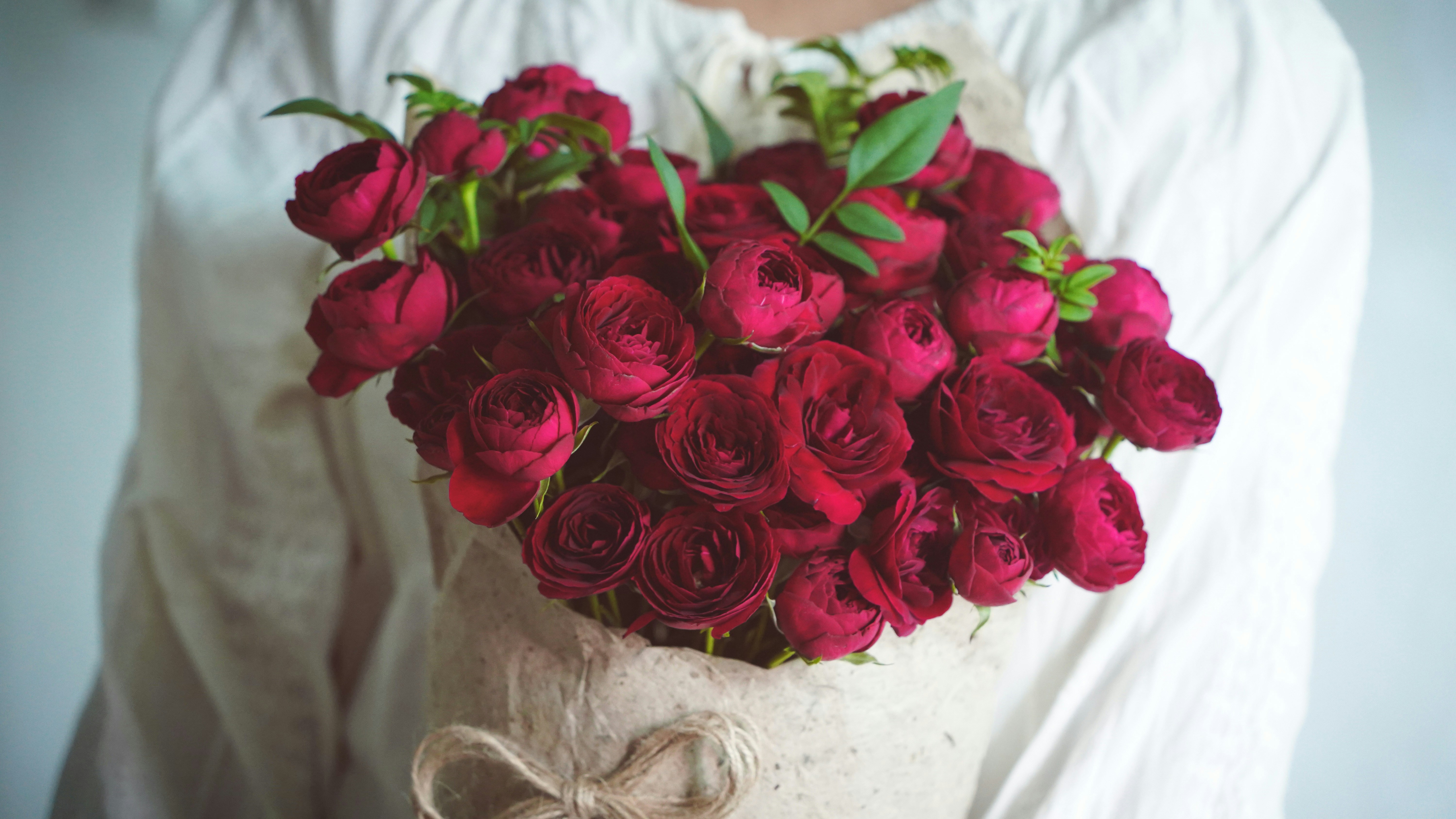 Soft-focus bouquet of deep red roses held against a light, flowing fabric backdrop; a creamy lace wrap surrounds the stems, suggesting a bridal or ceremonial arrangement.