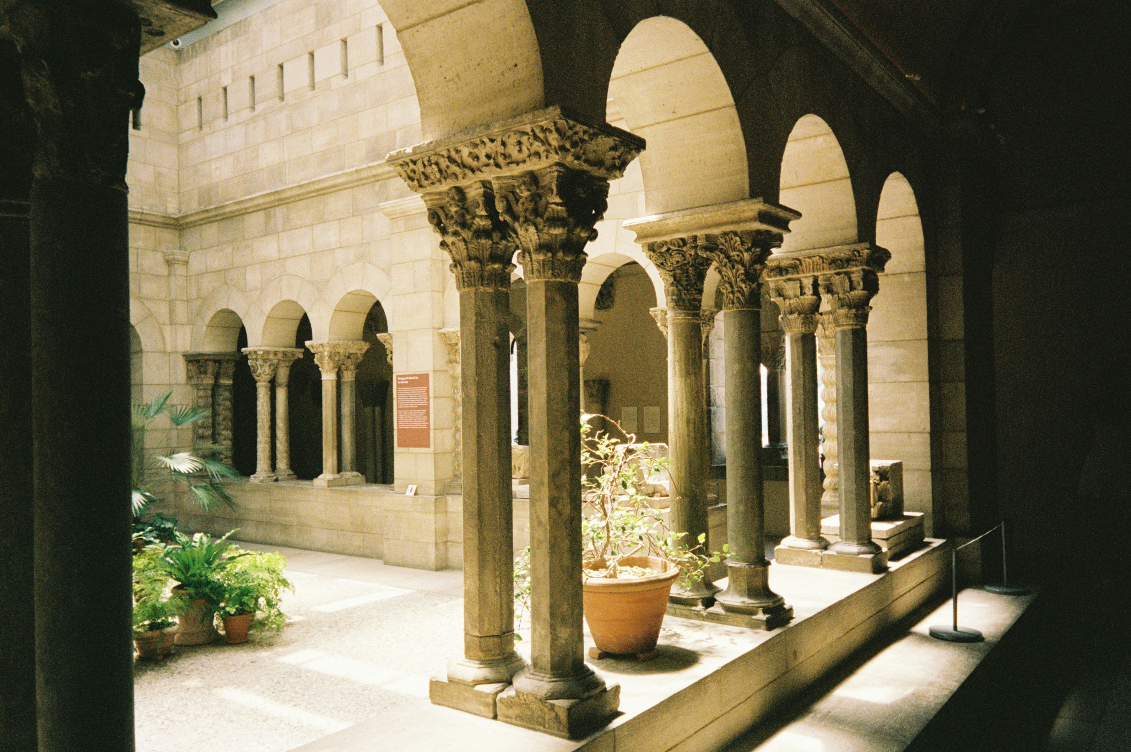 Stone arches and carved columns in a sunlit medieval cloister with potted plants