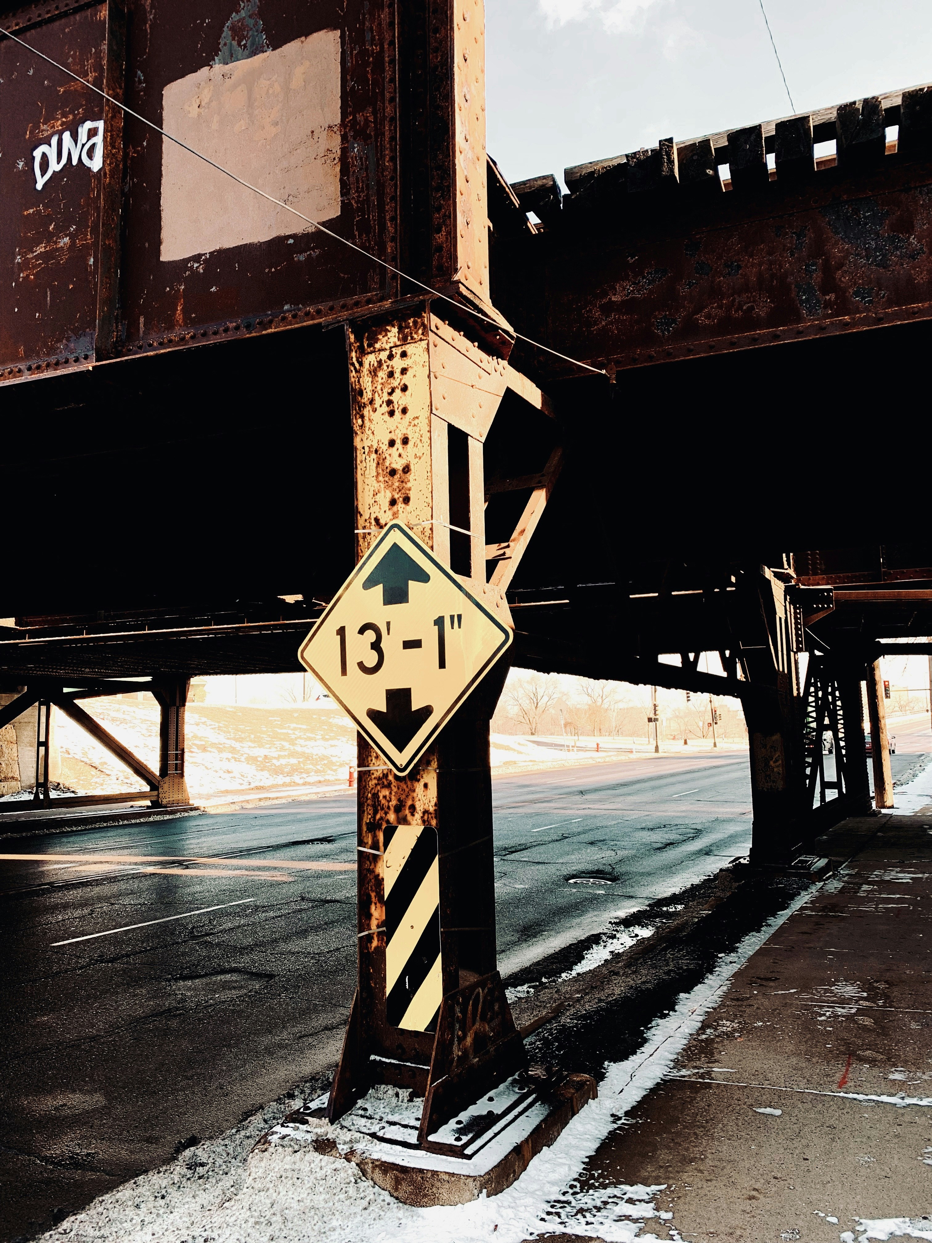 Rust Gate and Signpost Under an Industrial Overpass