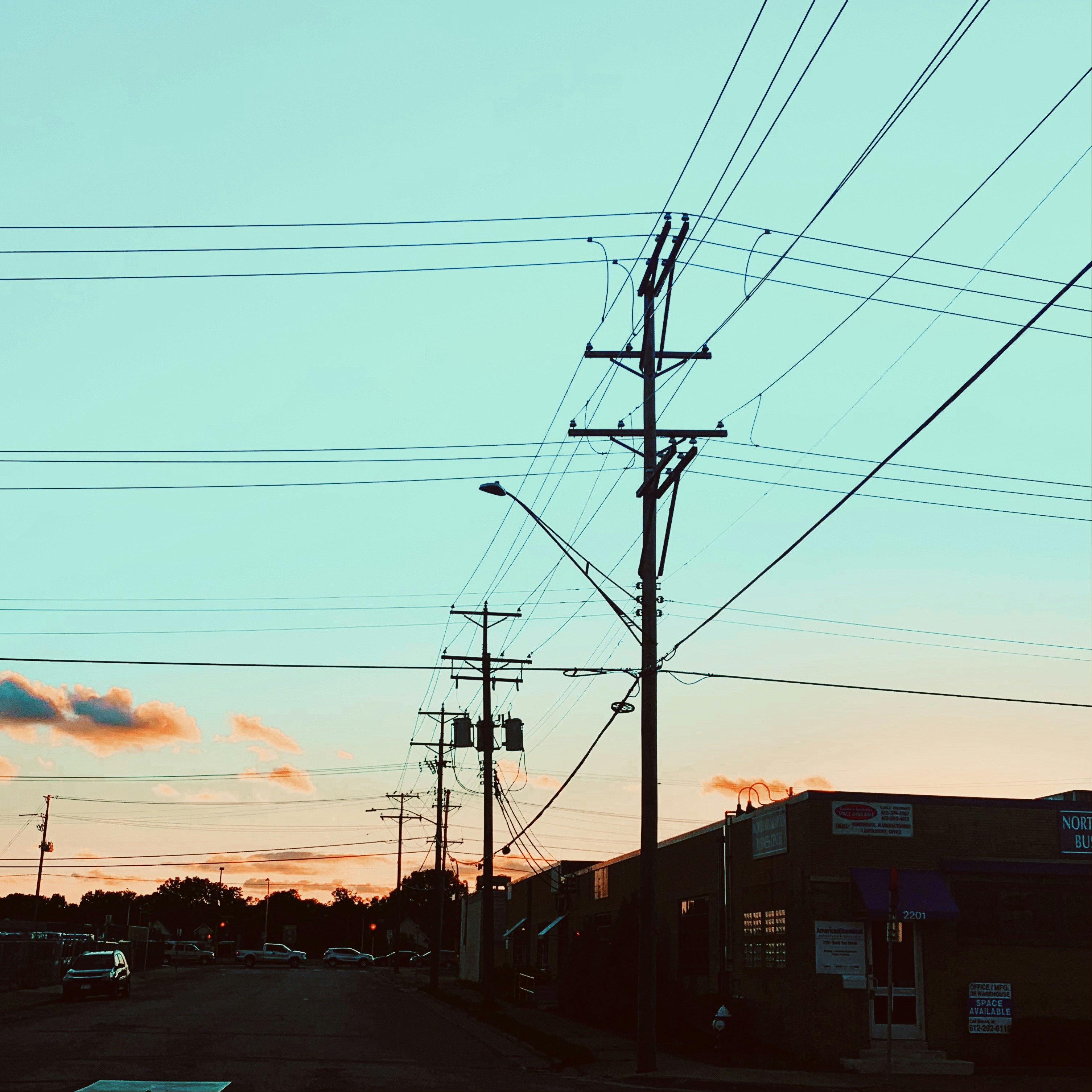 Sunset-tinged street scene with utility poles and power lines lining a storefront row.