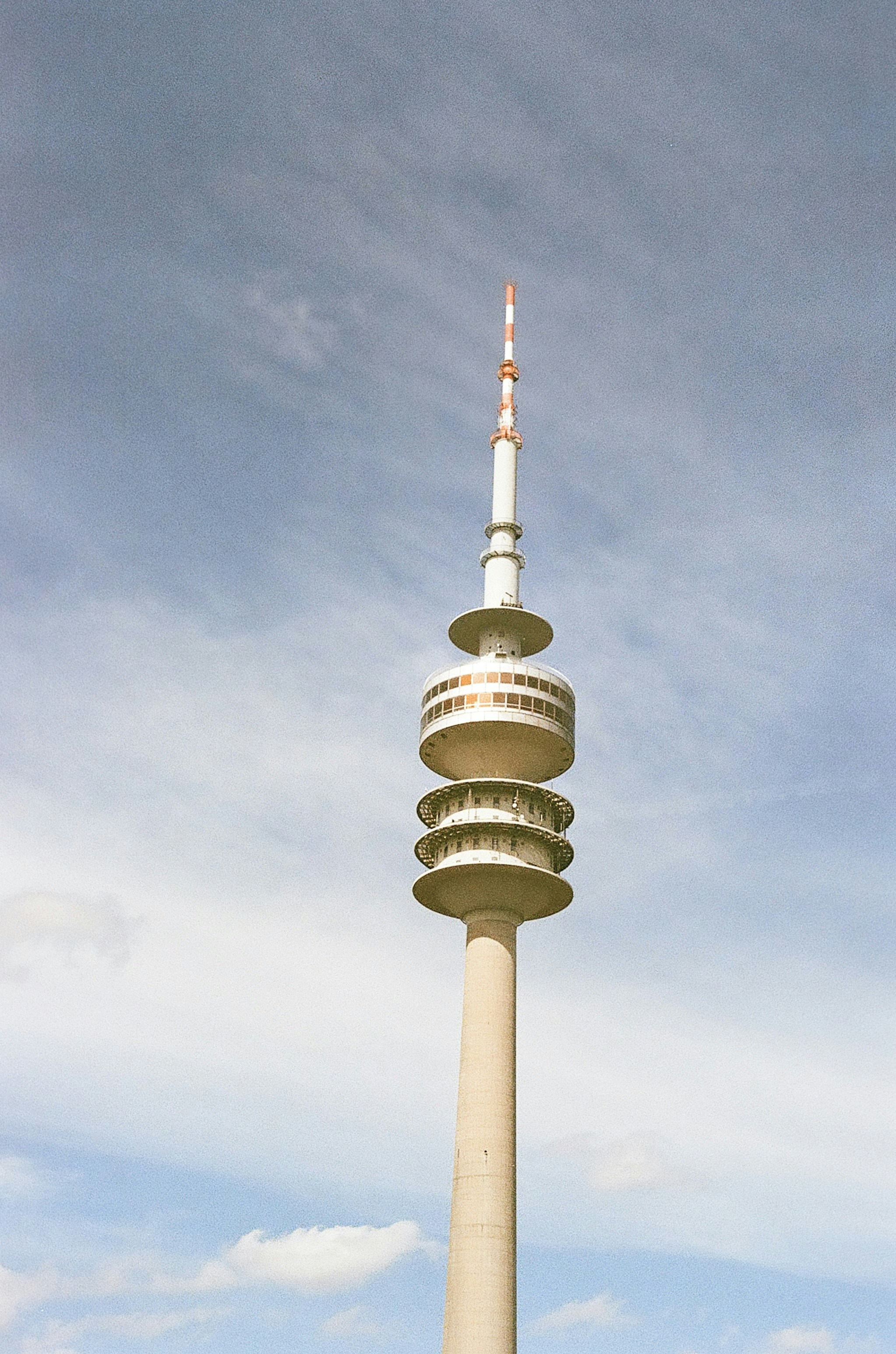 Tall telecommunications tower piercing a clear blue sky with wispy clouds. A minimalist architectural subject emphasizing height and geometric forms.