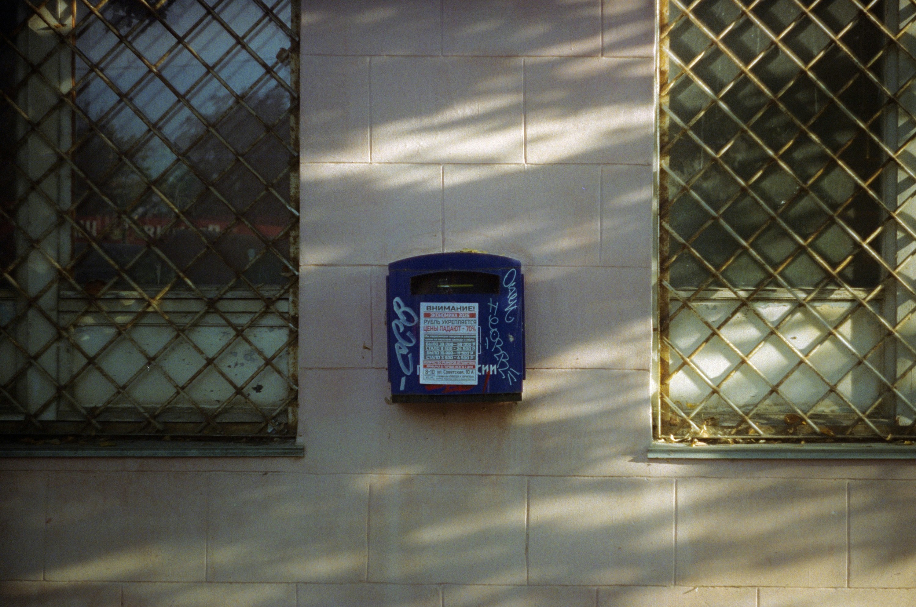Blue mailbox centered on sunlit tiled wall between barred windows