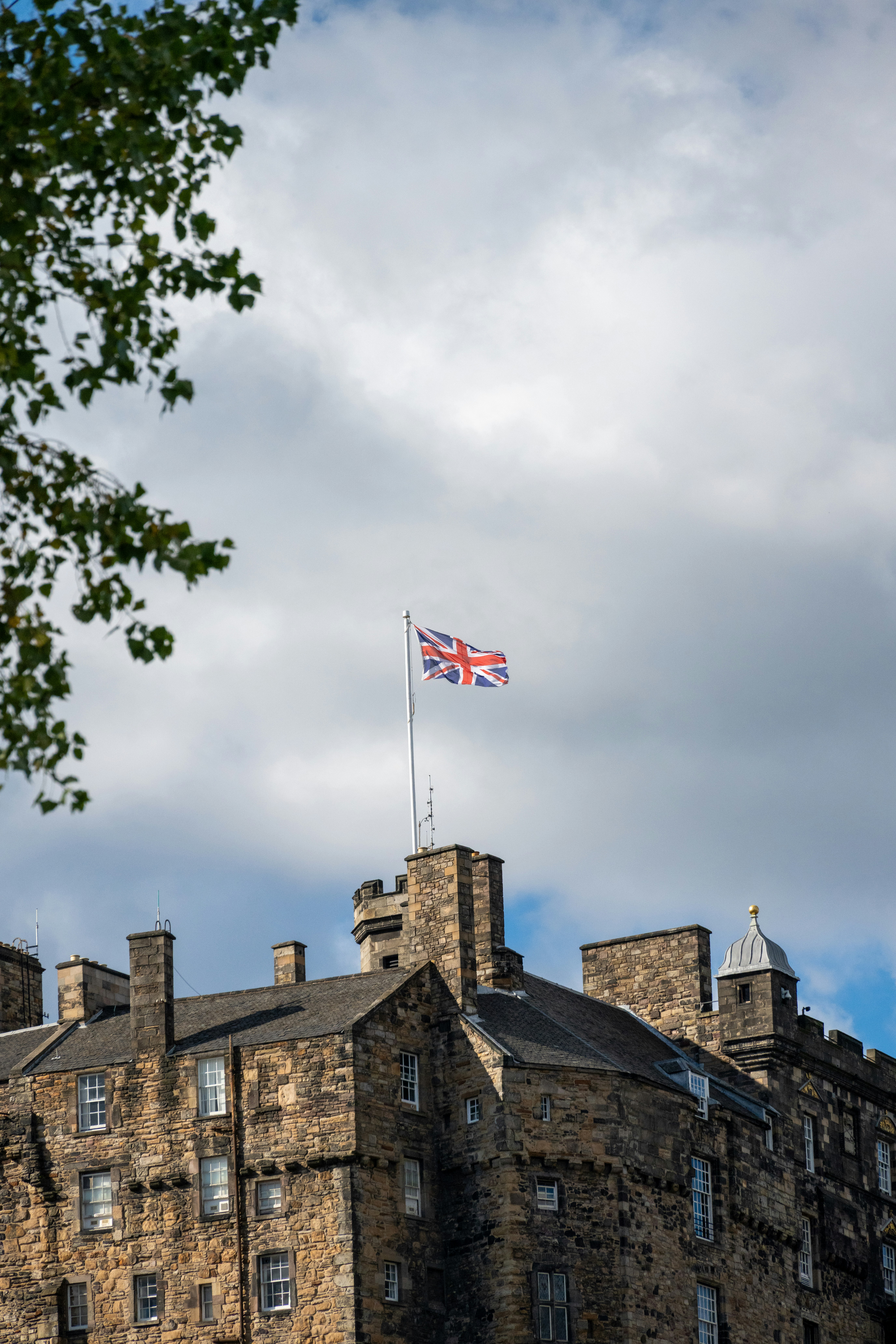 Flag over stone fortress: a timeless Union Jack atop a weathered castle under a drift of clouds