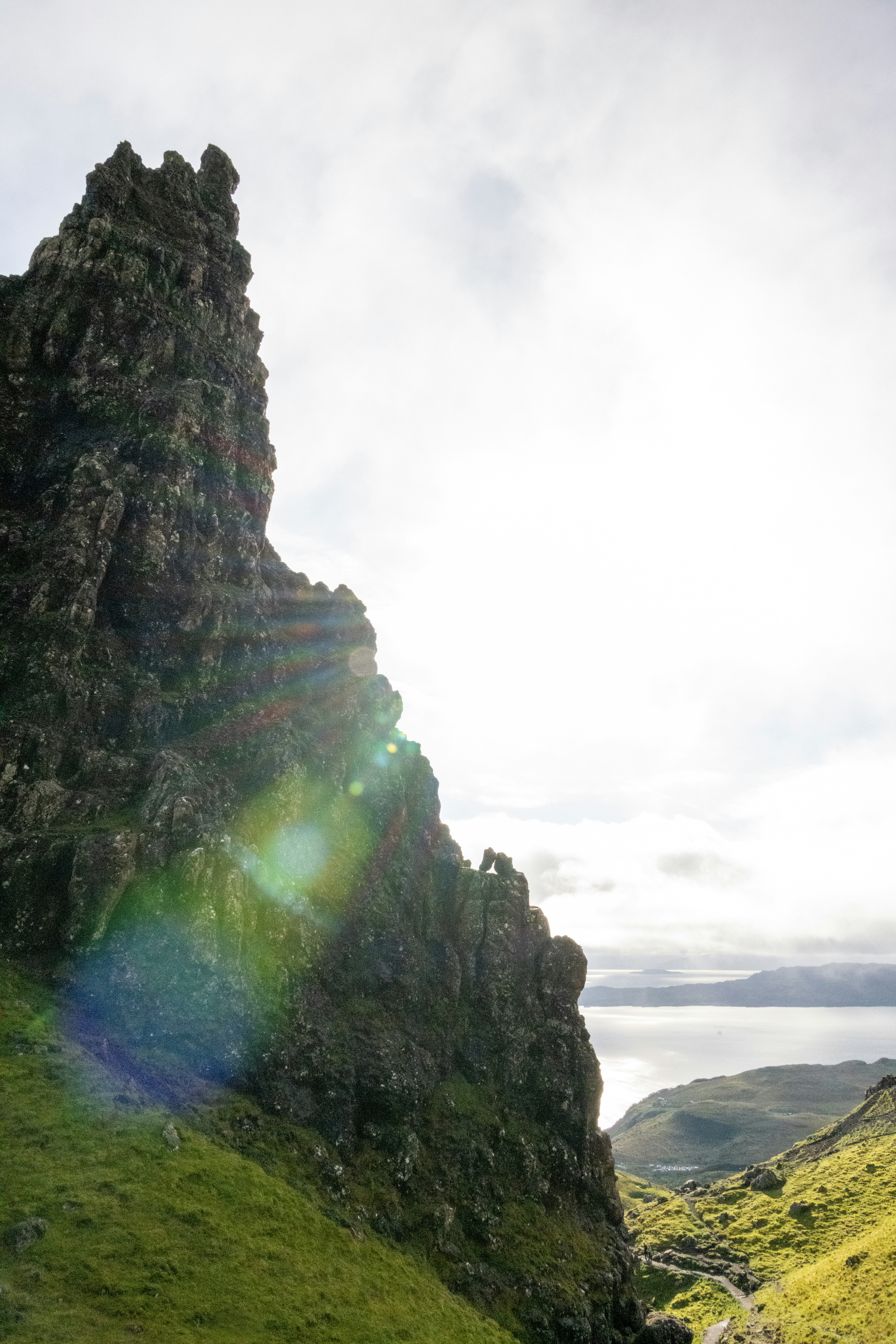 A towering basalt cliff at golden hour with lens flare over a rugged hillside