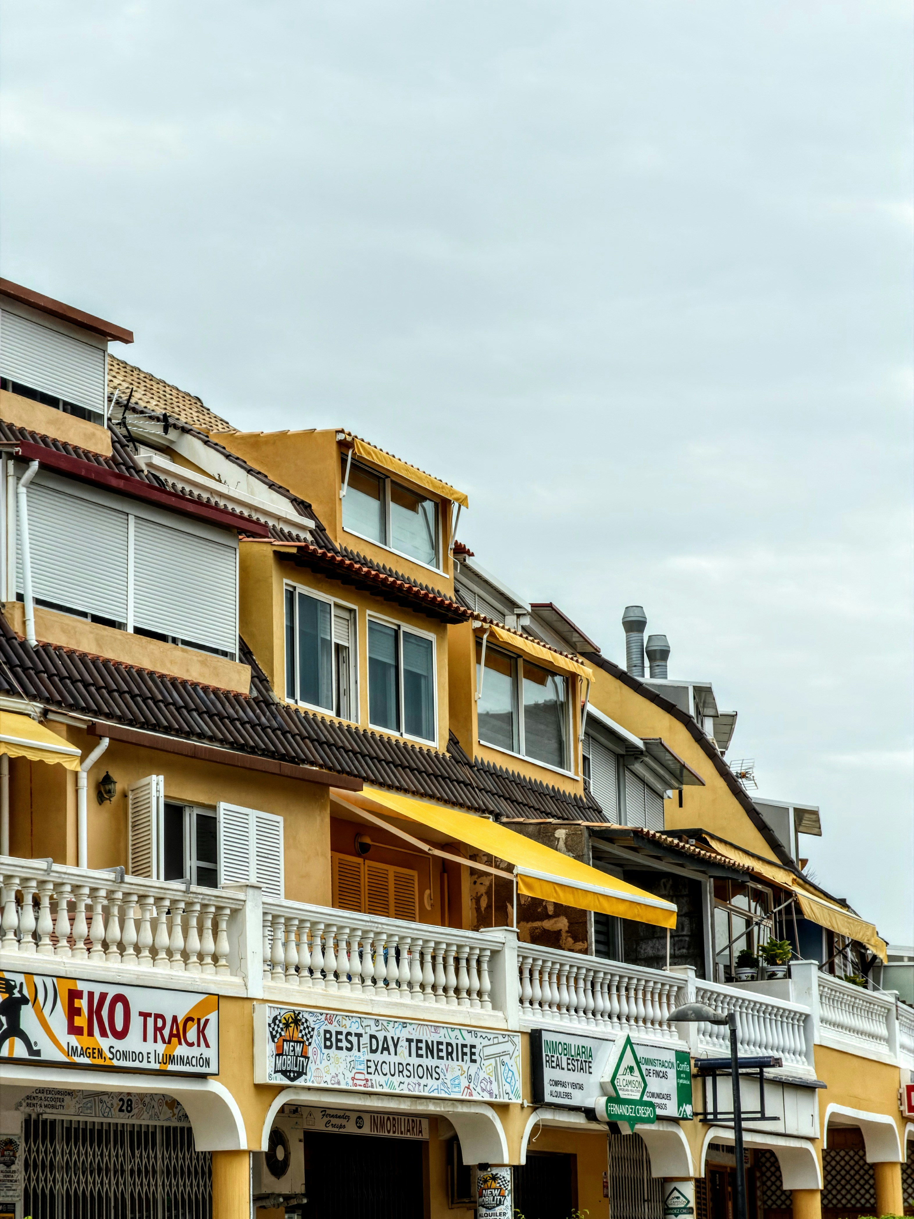 Colorful building facades with awnings line a street, balconies, and storefronts under a pale sky.