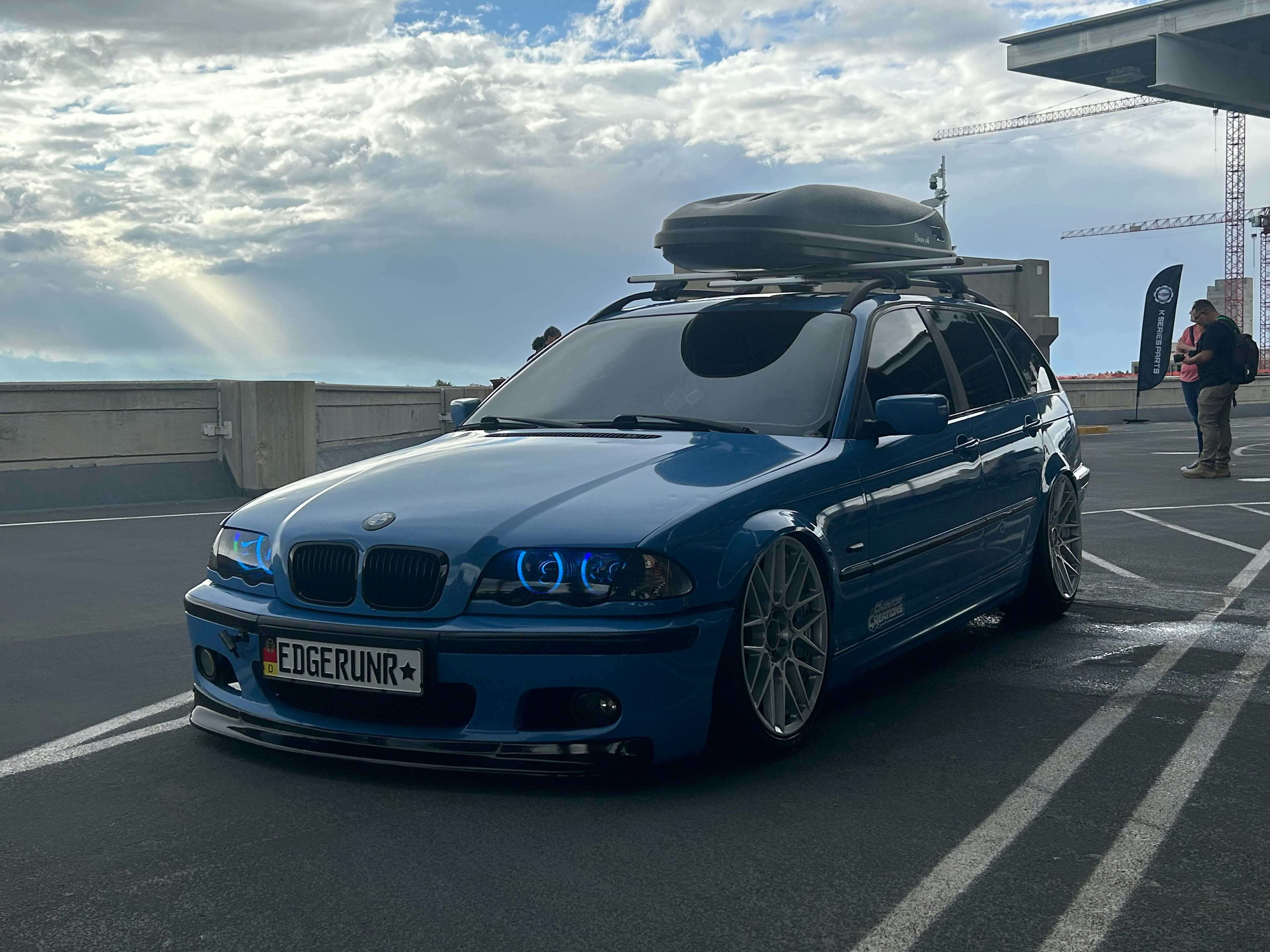A blue station wagon with a roof cargo box parked on a concrete lot