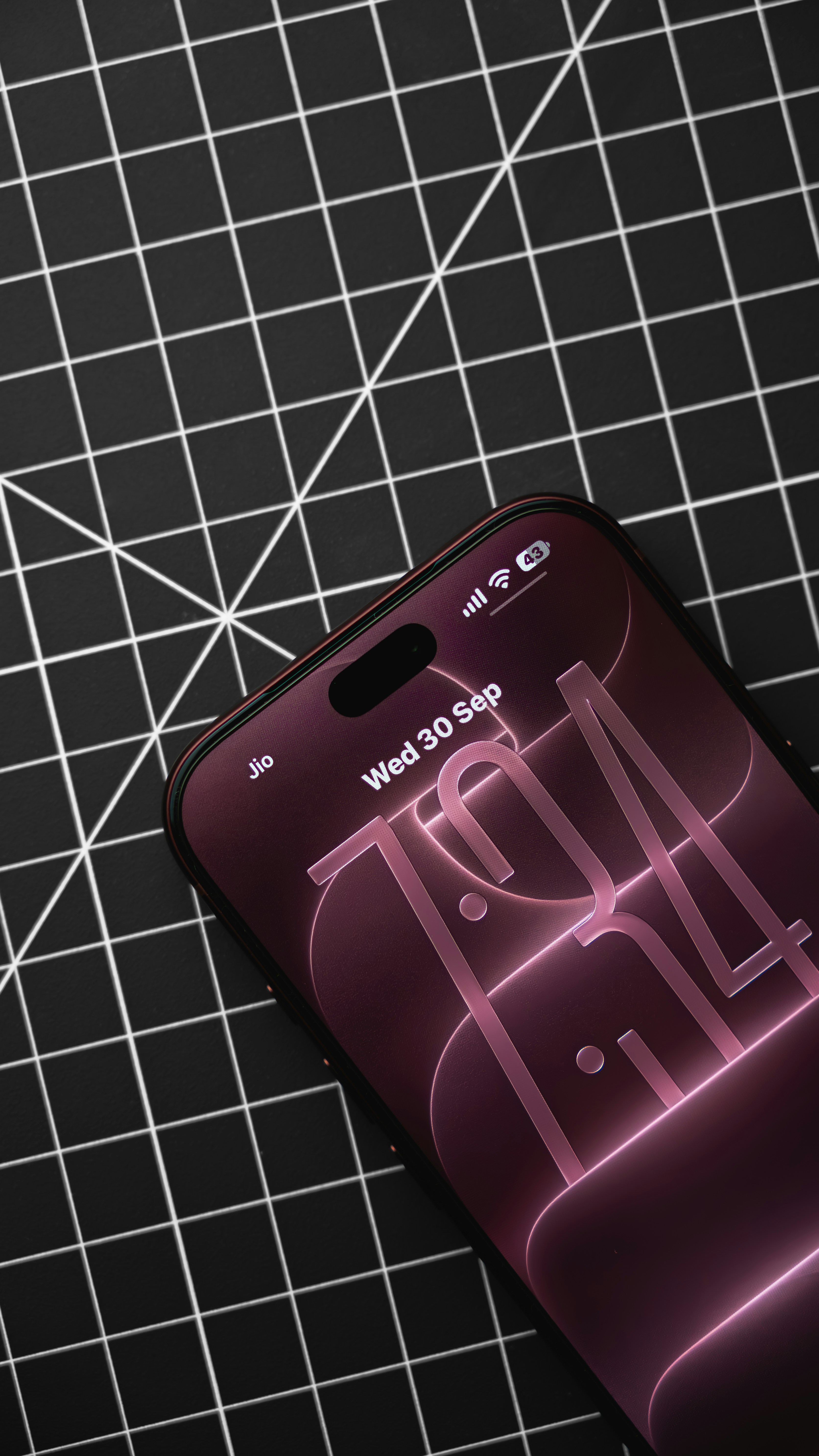 Close-up of a curved smartphone screen displaying a neon pink clock-like graphic on a dark background with a grid pattern. The device rests diagonally, emphasizing the glow and sleek edges.