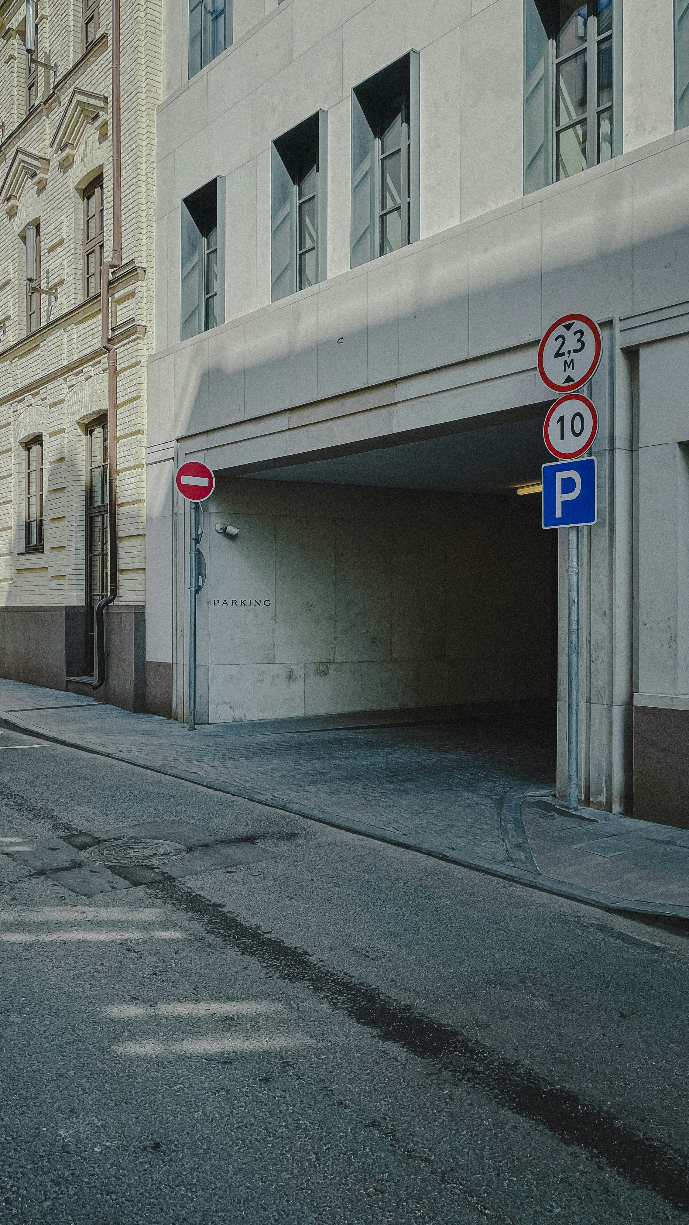 A concrete building entrance framed by a street with signage and a dark underpass, captured in daylight. This is a street scene with architectural textures and a sense of urban depth.