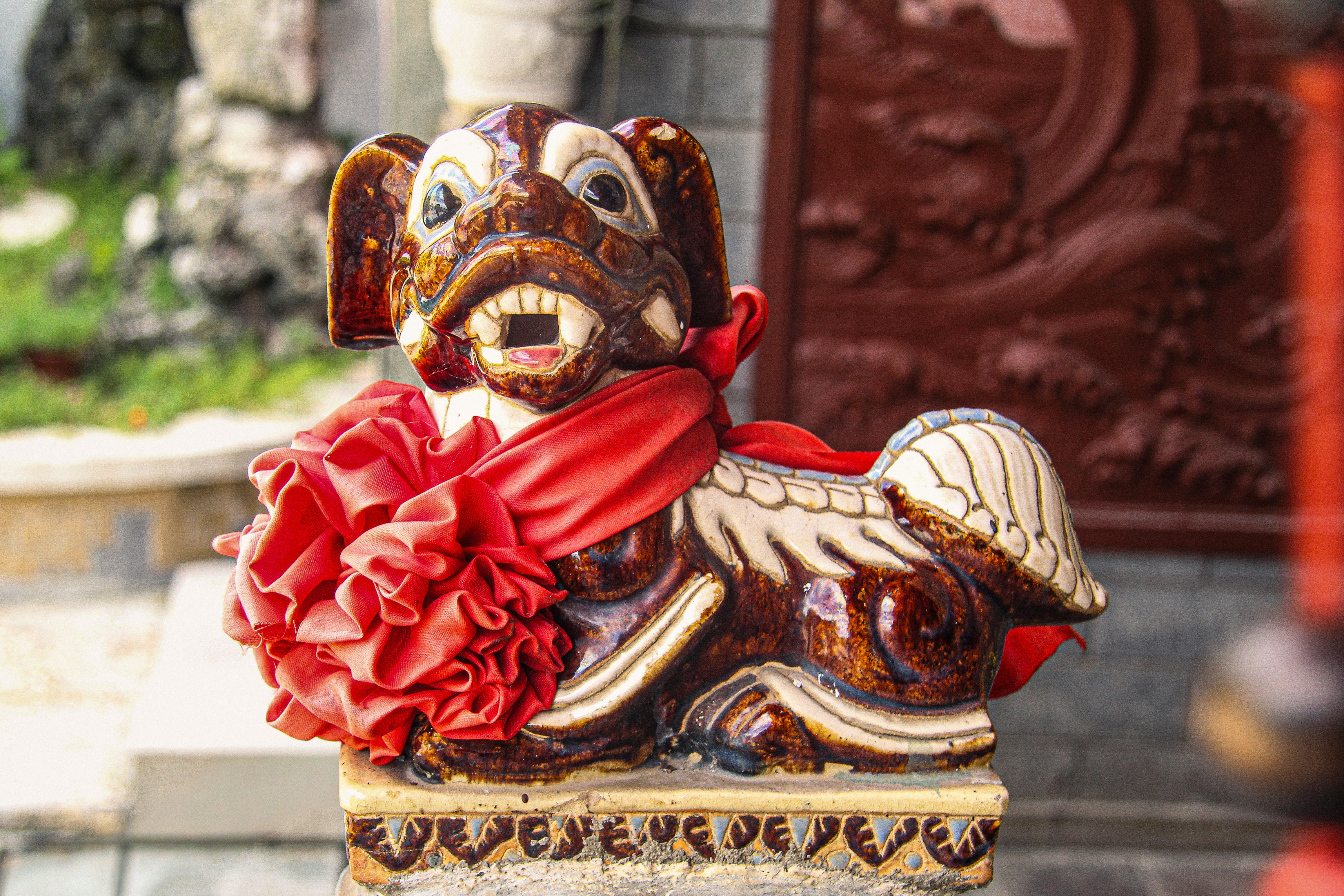 Scarlet blossom guardian: a carved canine statue with red ribbon on a temple plinth