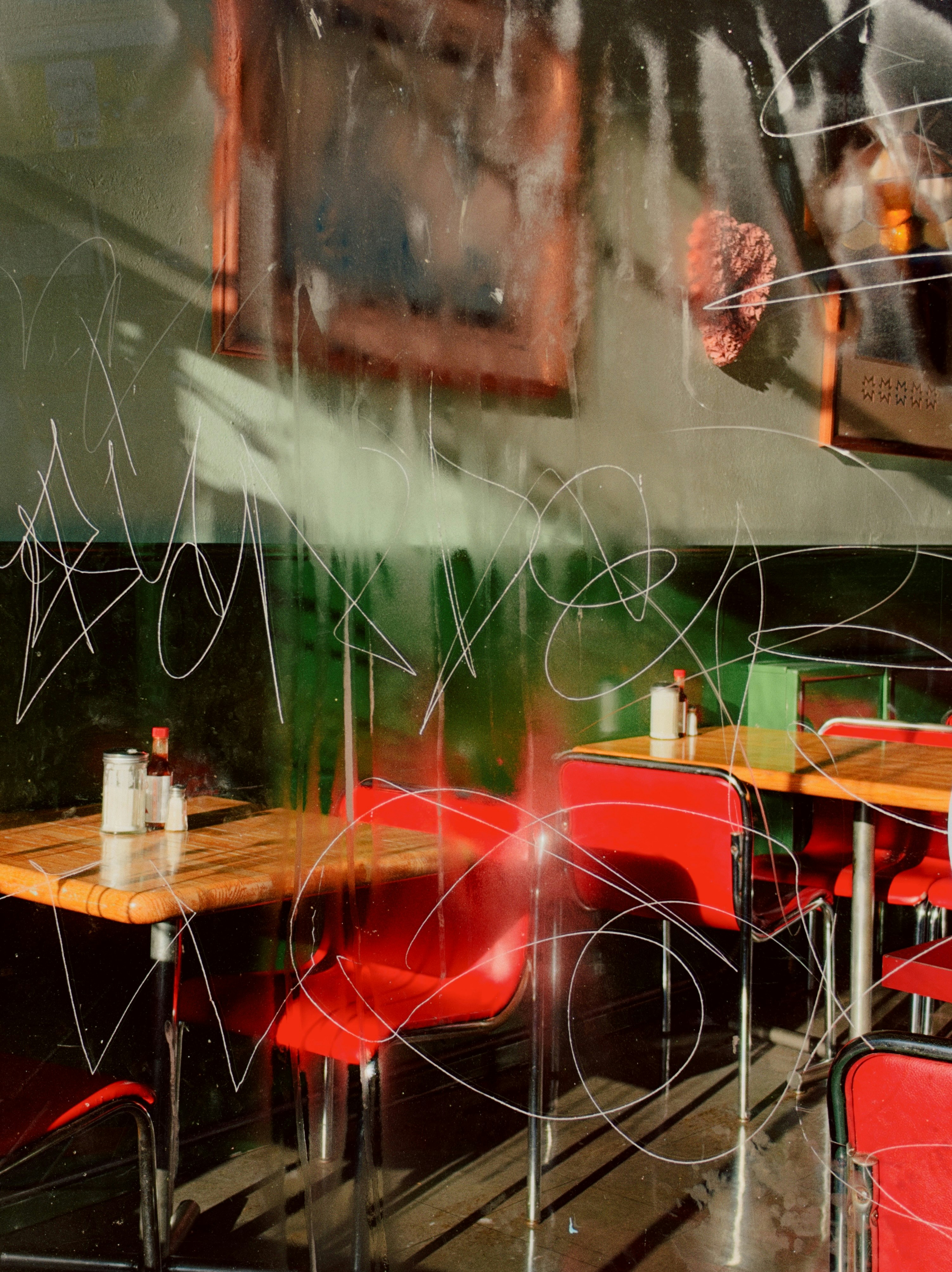 A diner interior with red chairs and wooden tables seen through scratched glass