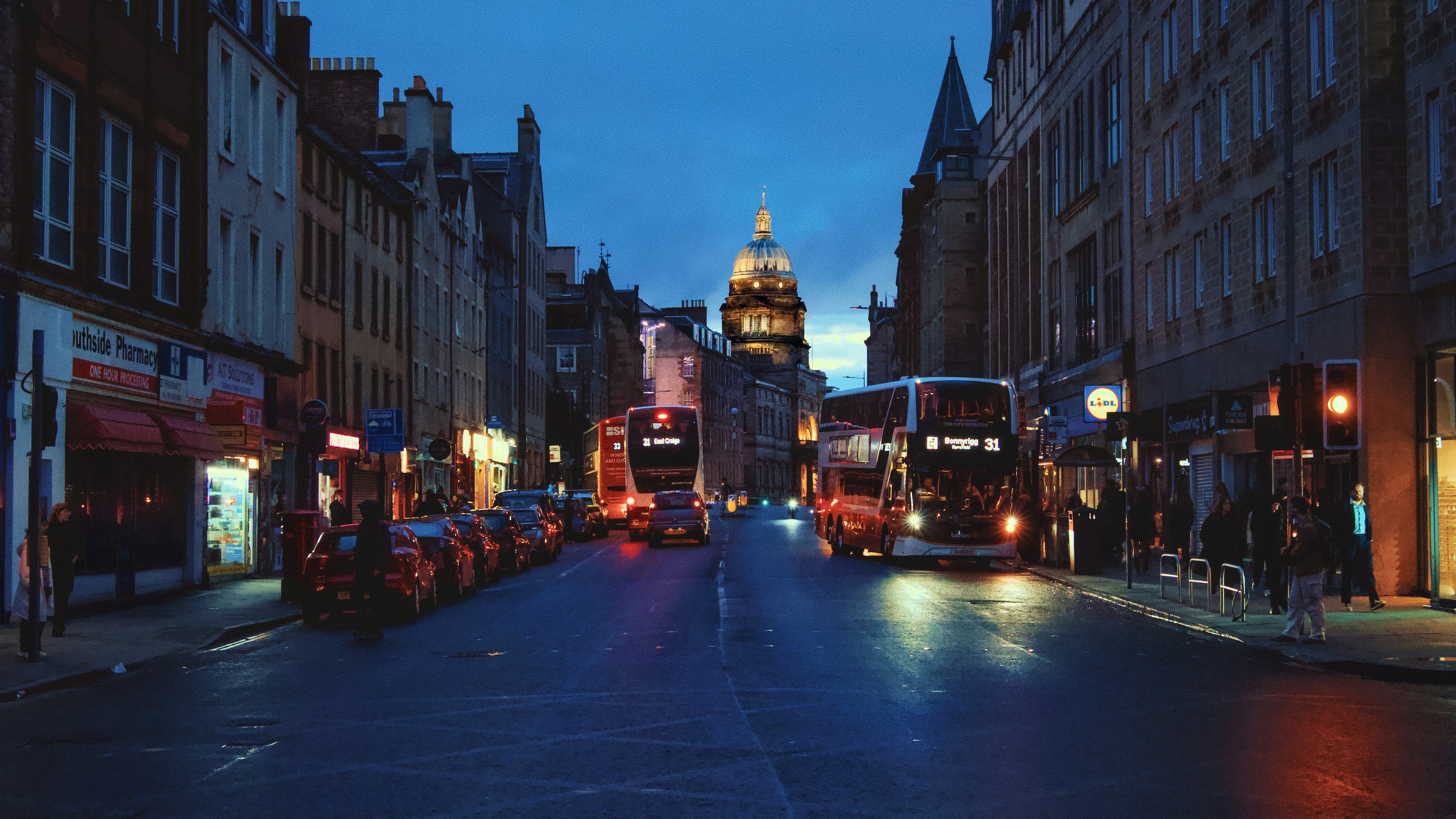 Nightfall on a Historic Street: Buses, Neon, and a Clocktower Glow