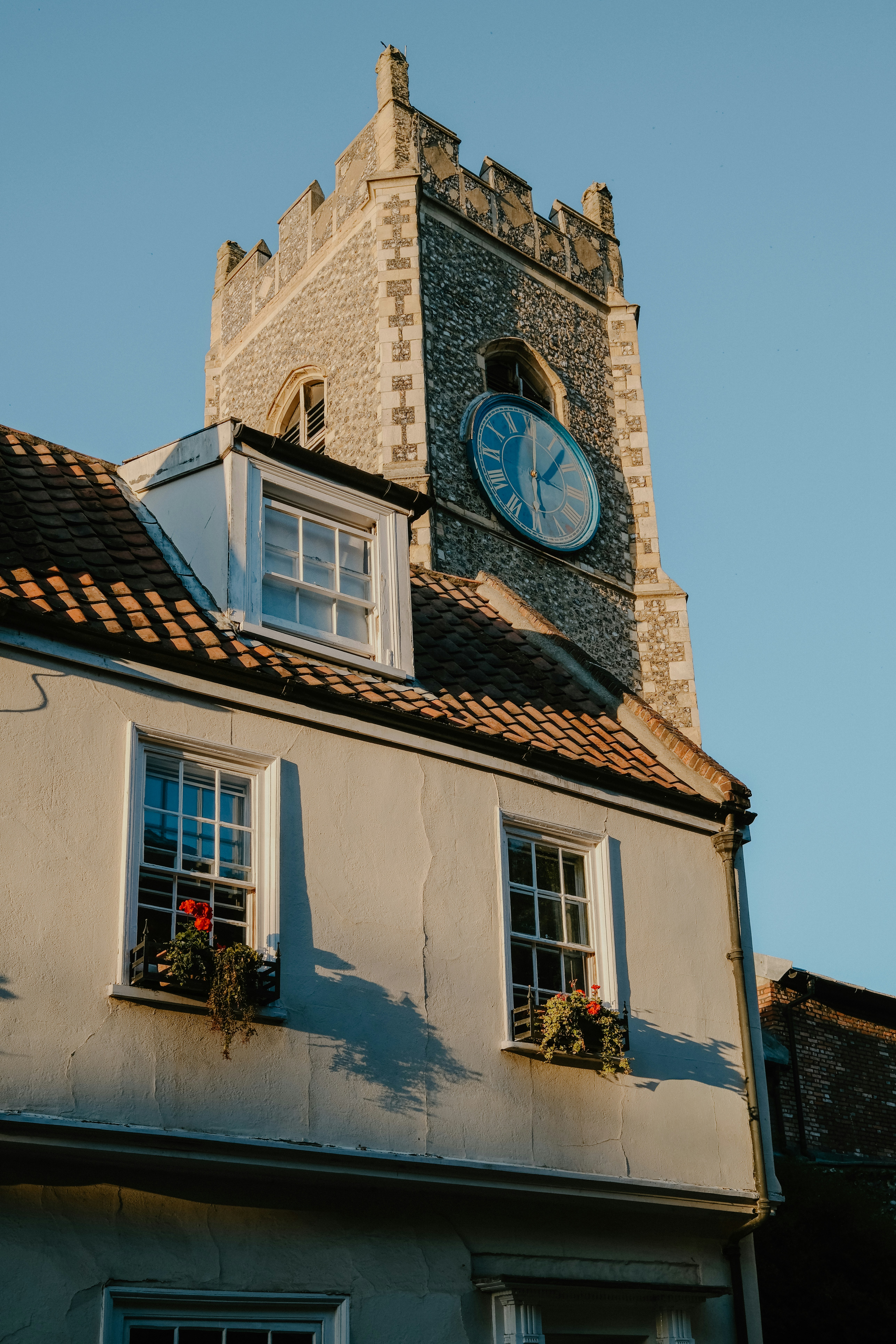 Clock Tower Over Looking Cottage: Sunlit Facade and Flowered Windows