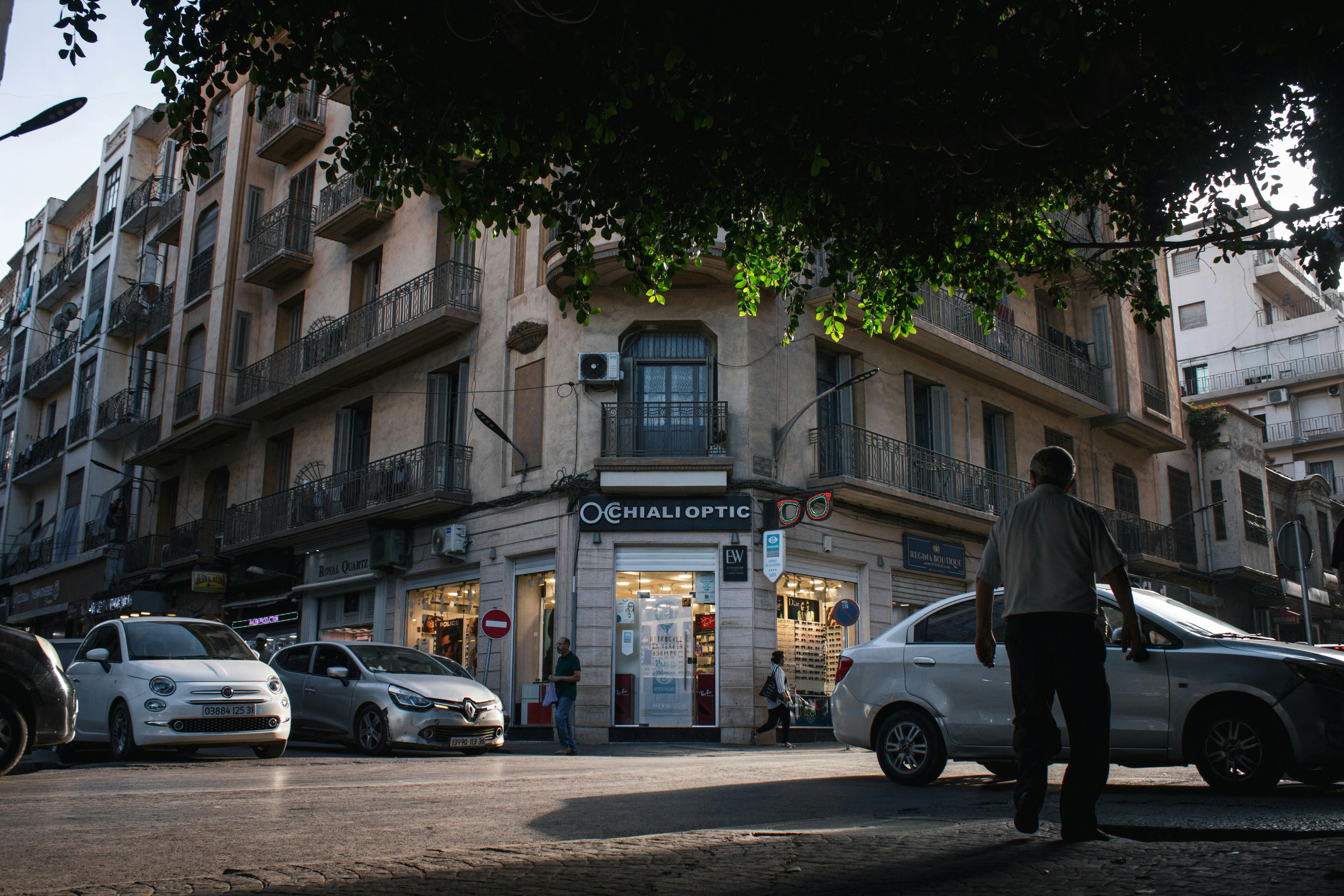 Sunlit Street Corner: A Pedestrian Walks Past a Ground-Level Shopfront at Dusk