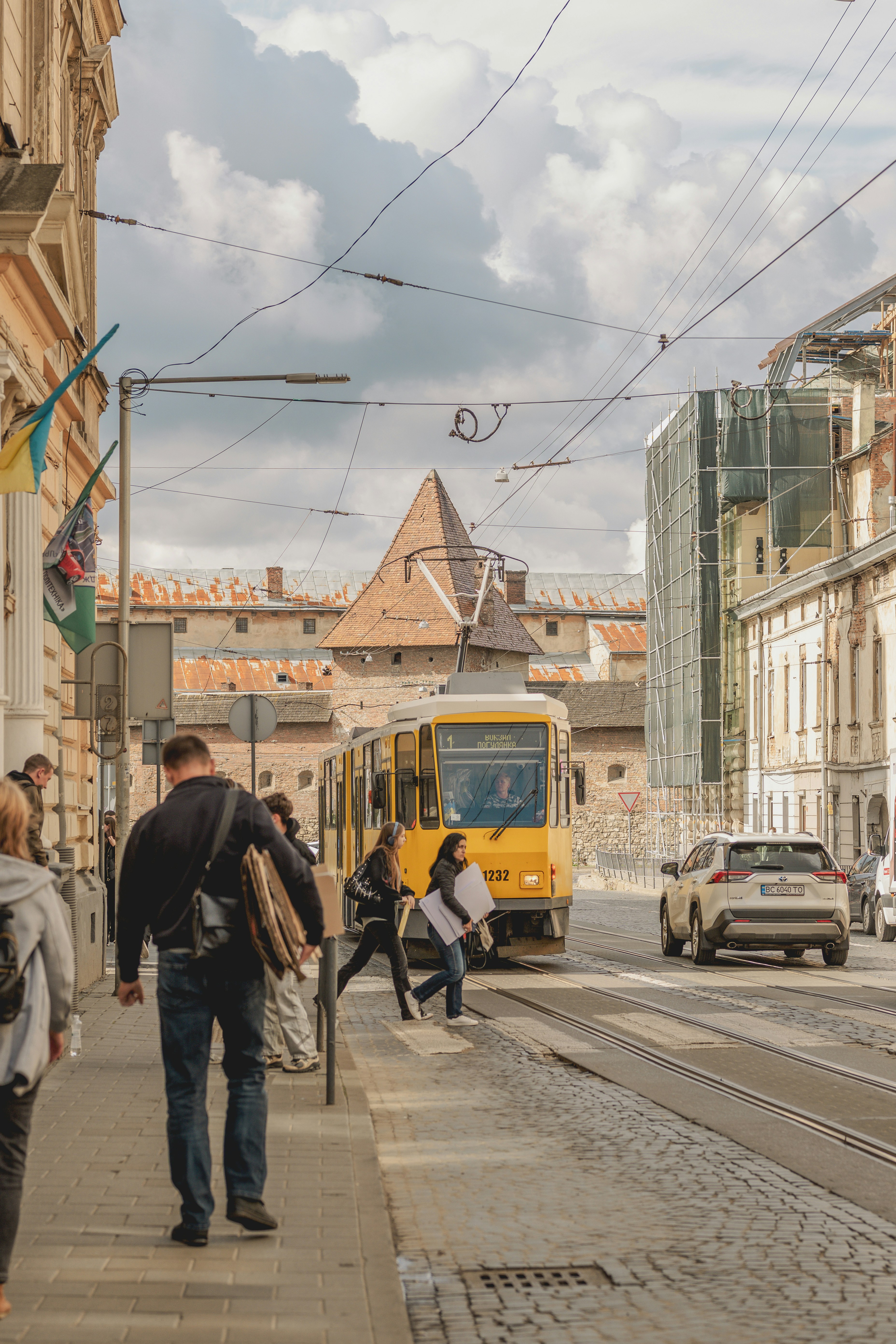 Yellow Tram in a European Street with Pedestrians and Historic Rooflines